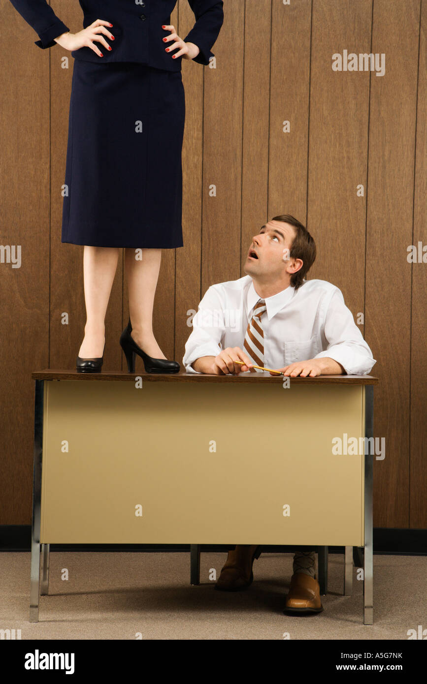 Mid adult Caucasian male sitting at desk looking up to Caucasian female ...