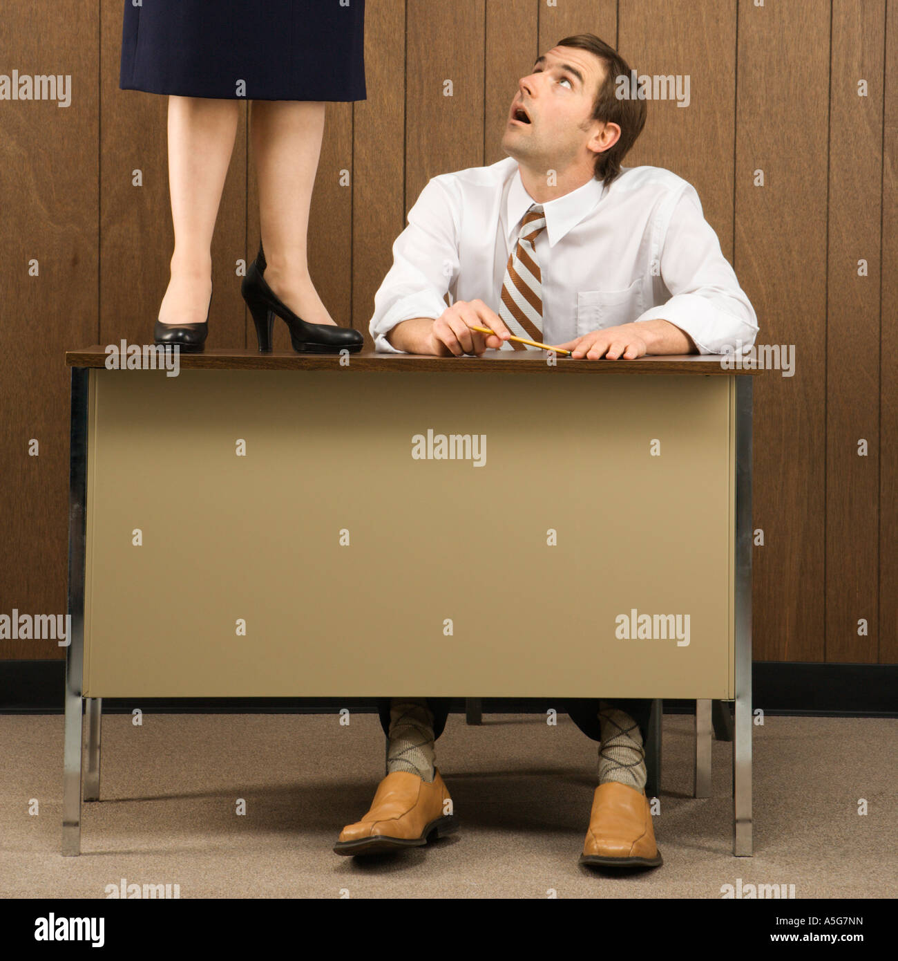 Mid adult Caucasian male sitting at desk looking up to Caucasian female ...