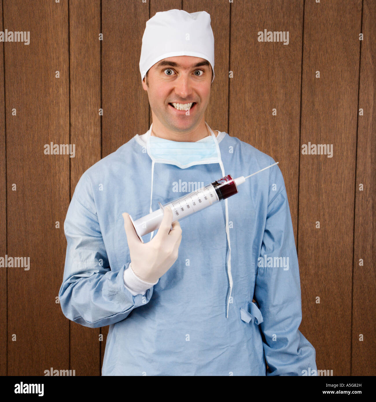 Mid adult Caucasian male surgeon holding oversized syringe and smiling ...
