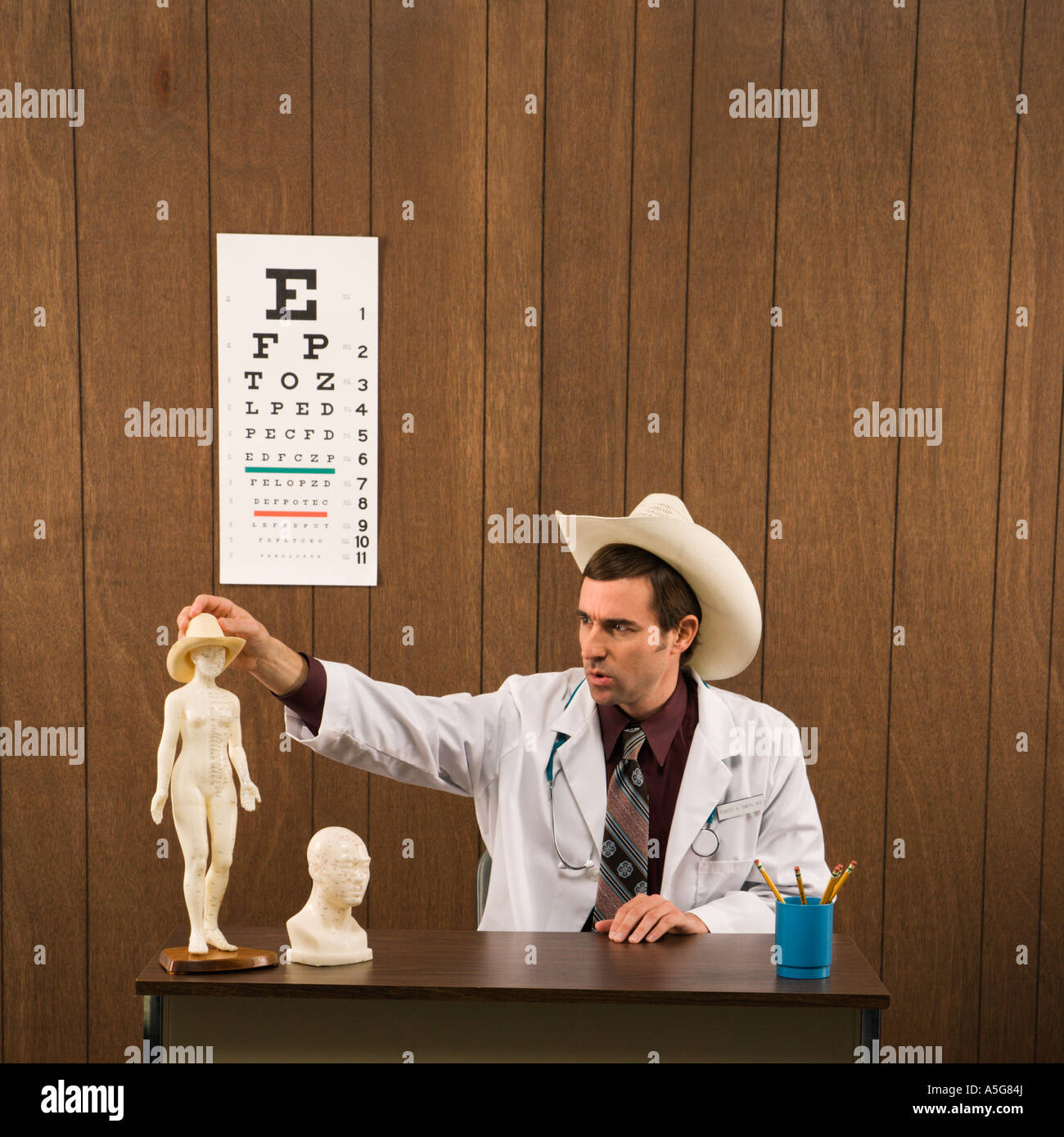 Mid adult Caucasian male doctor wearing cowboy hat sitting at desk ...