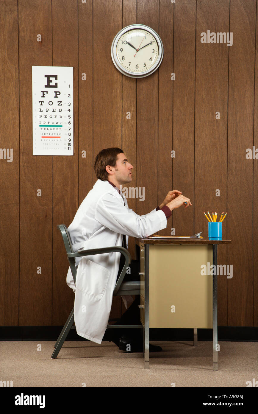 Side view of mid adult Caucasian male doctor sitting at desk Stock ...