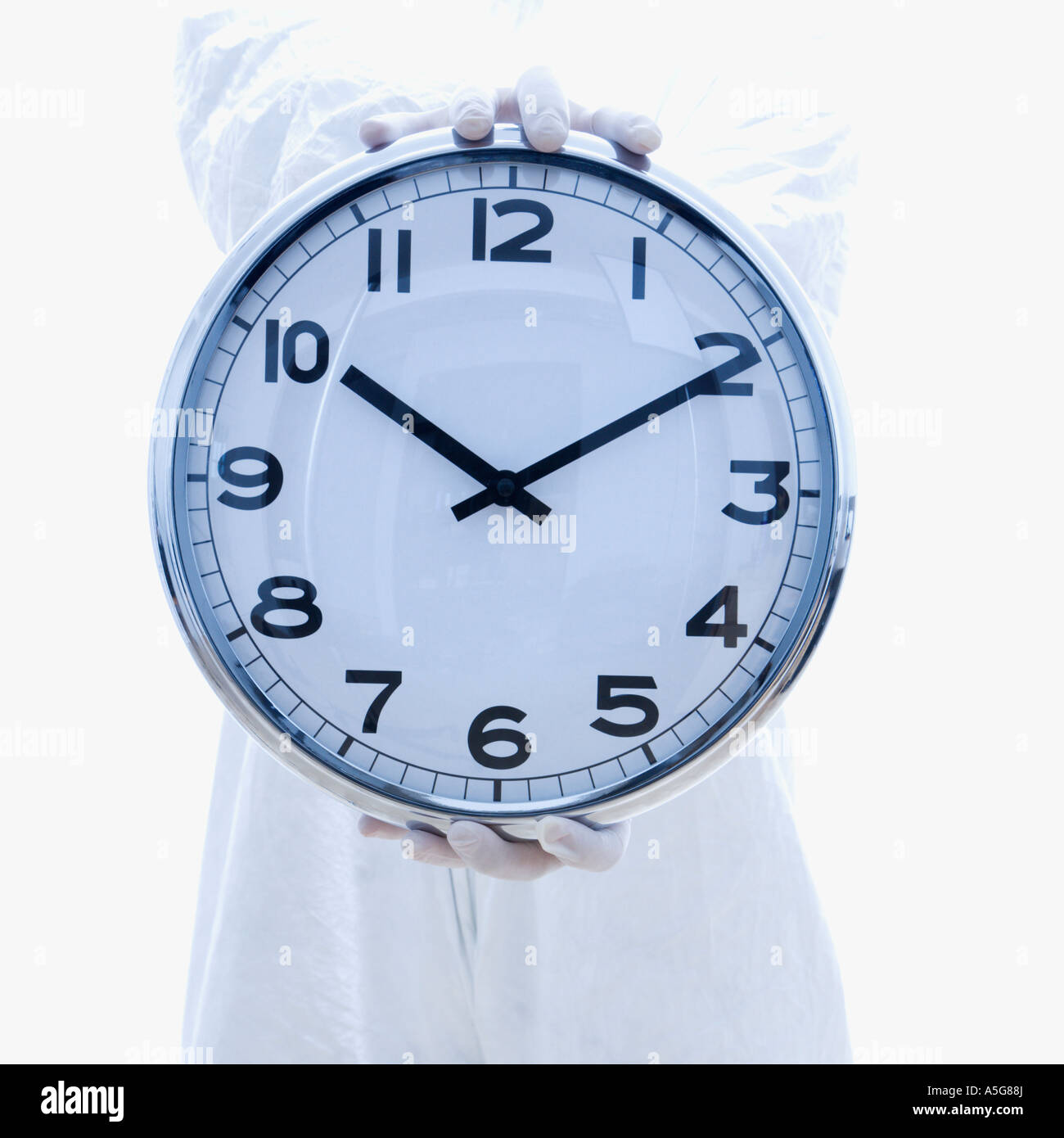Man in biohazard suit holding out clock standing against white ...