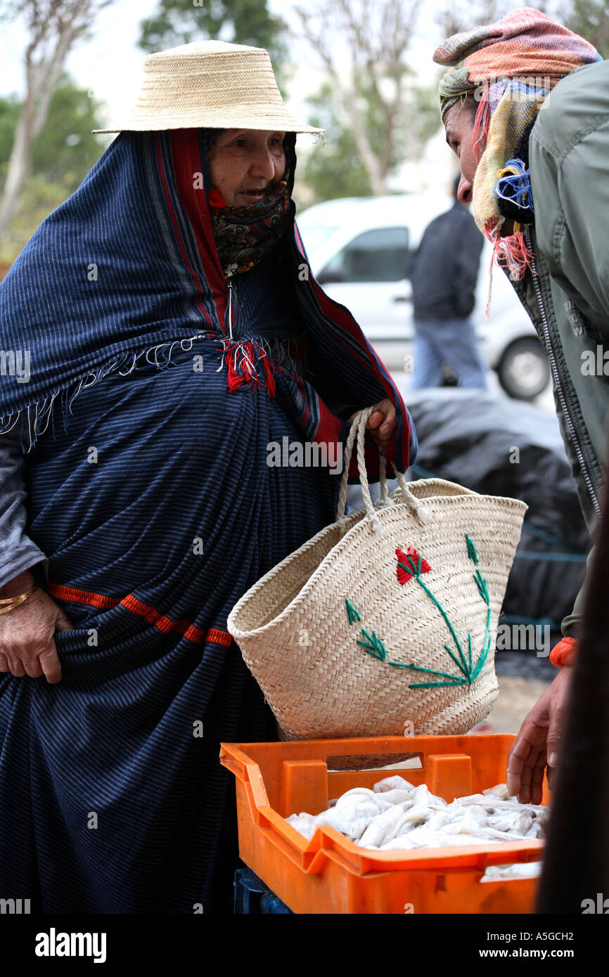 Vertical portrait of old berber woman in traditional dress buying fish ...