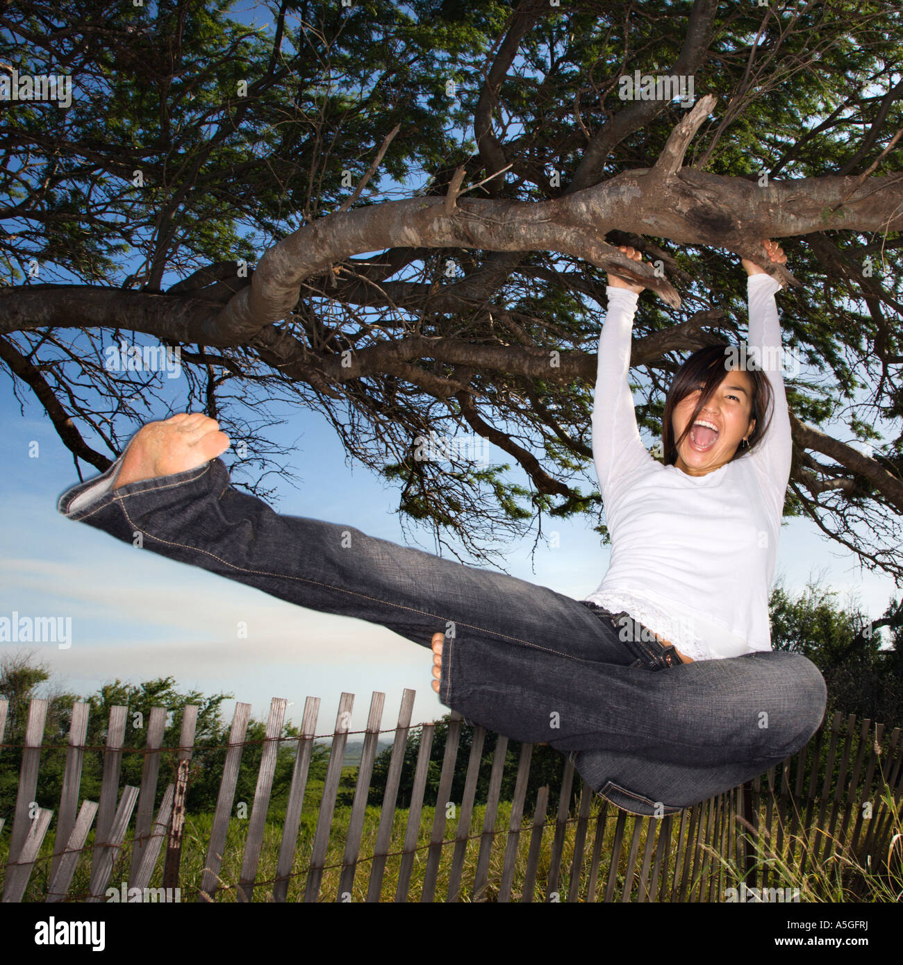Young adult Asian female holding on to tree and kicking air and ...