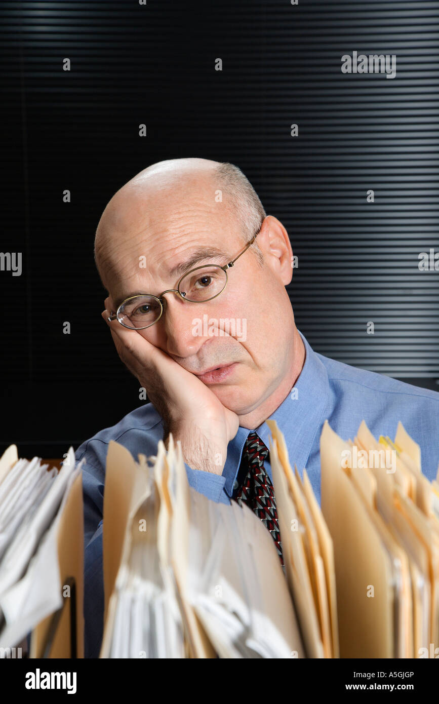 Caucasian middle aged businessman with files leaning head on hand ...