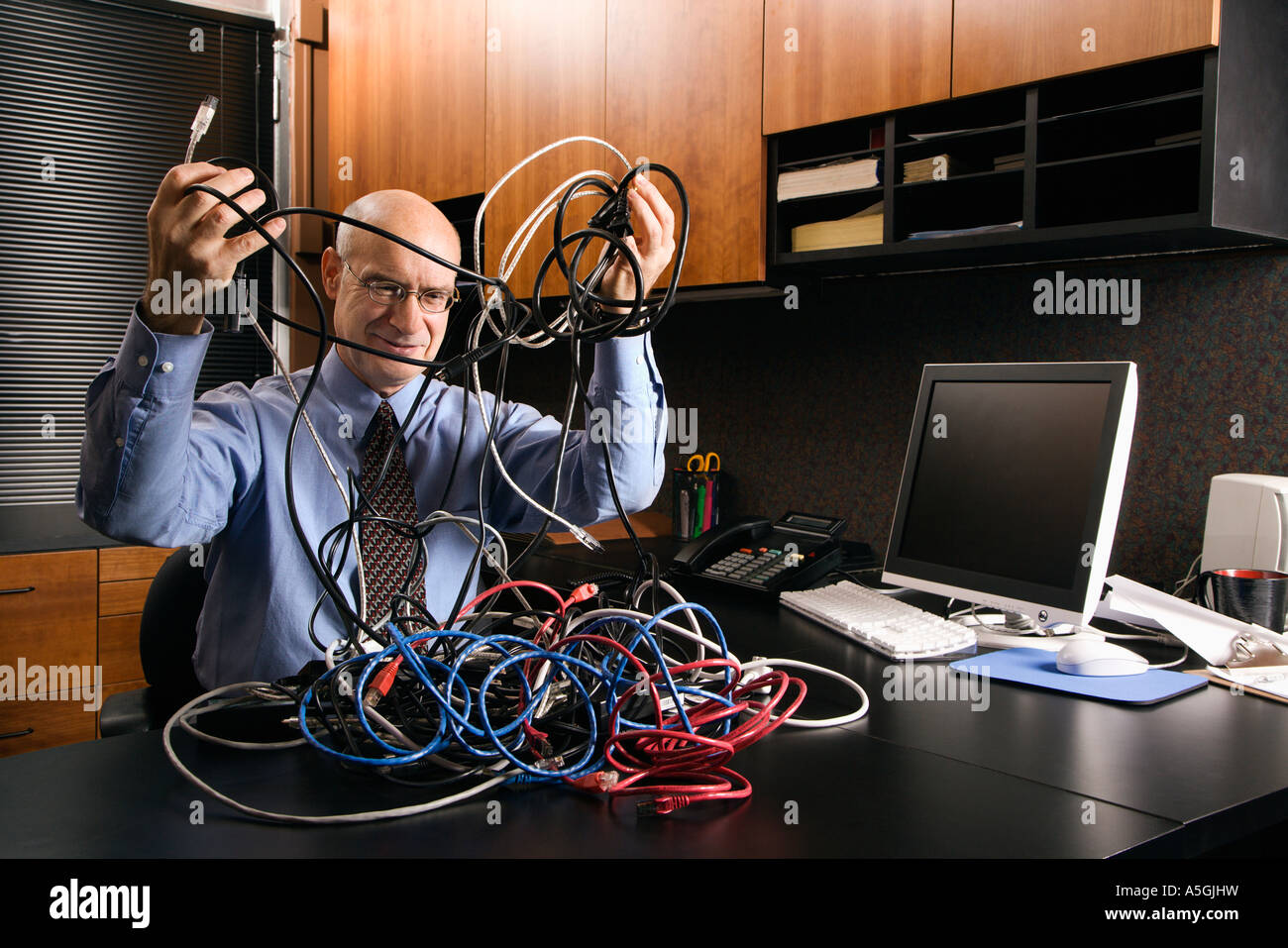 Caucasian middle aged businessman at desk in office with a tangle of ...