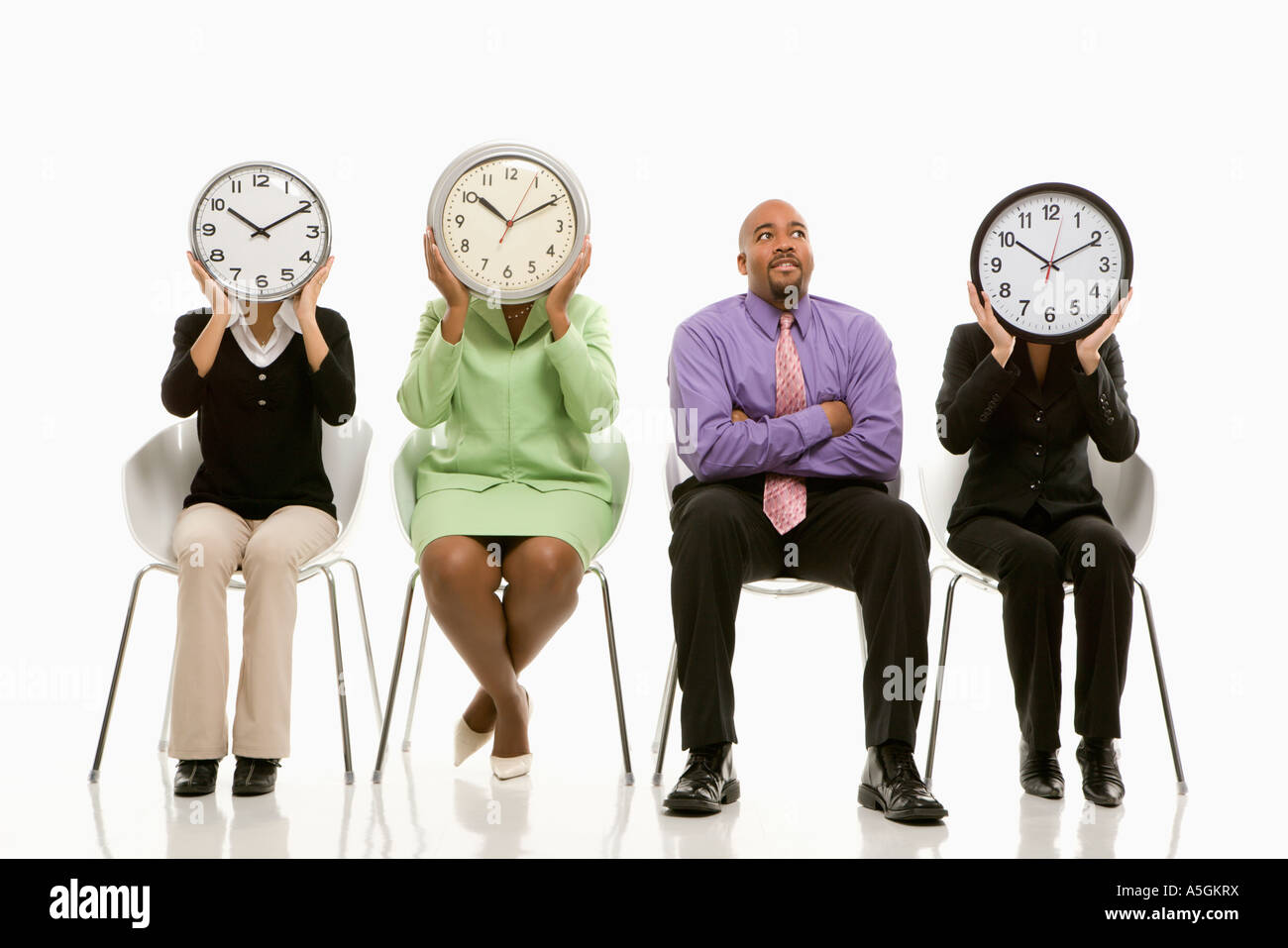 Businesswomen sitting holding clocks over faces while African American ...