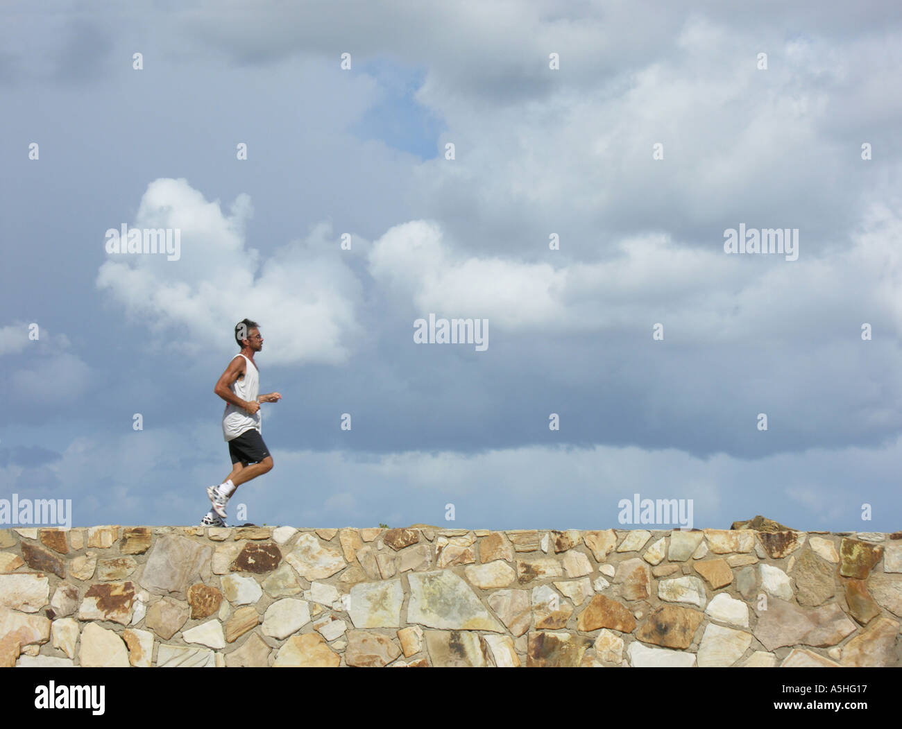 Runner in singlet jogging on stone wall Stock Photo - Alamy