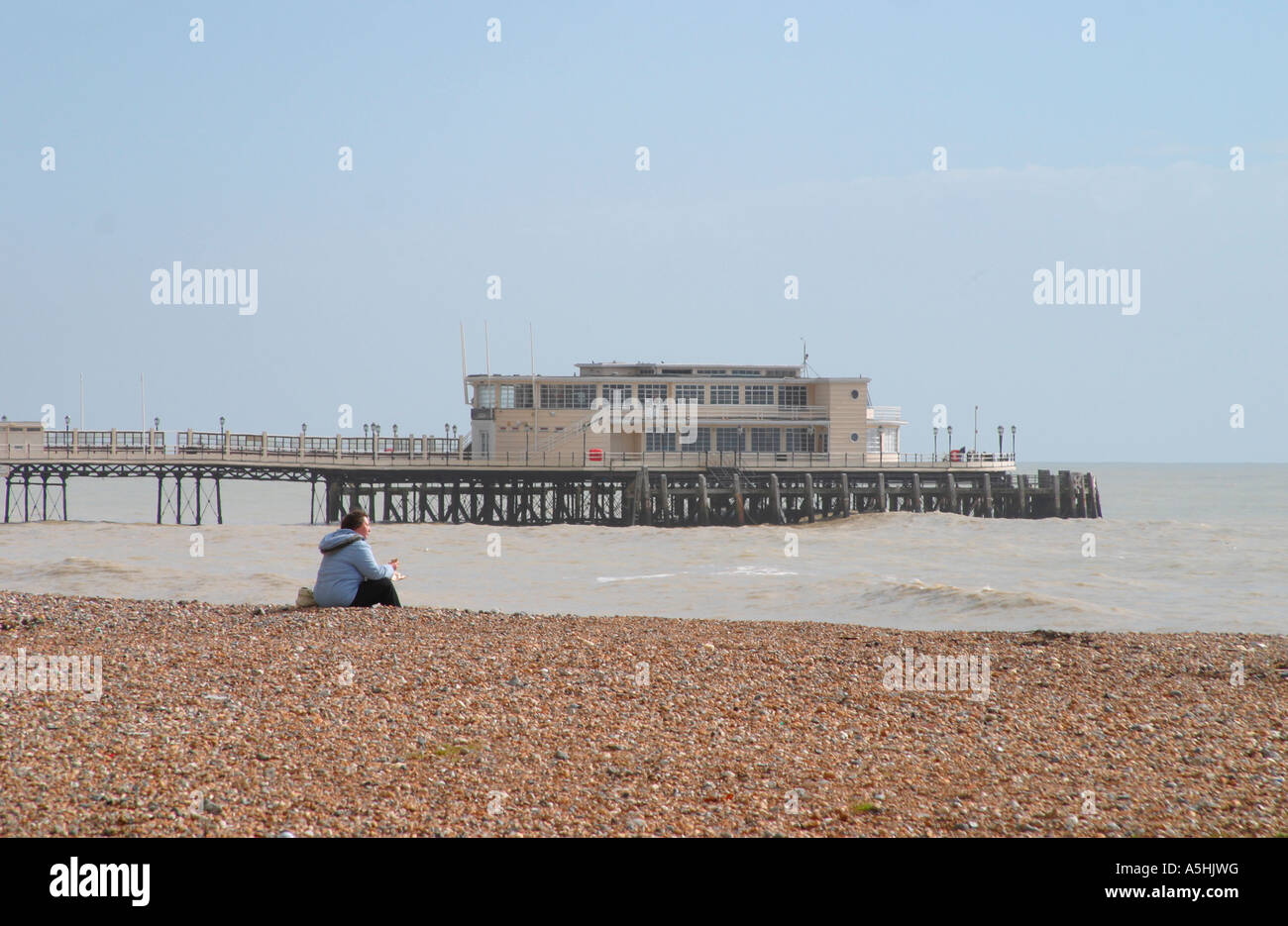 Lady sitting alone on shingle beach near Worthing Pier, Worthing, West ...