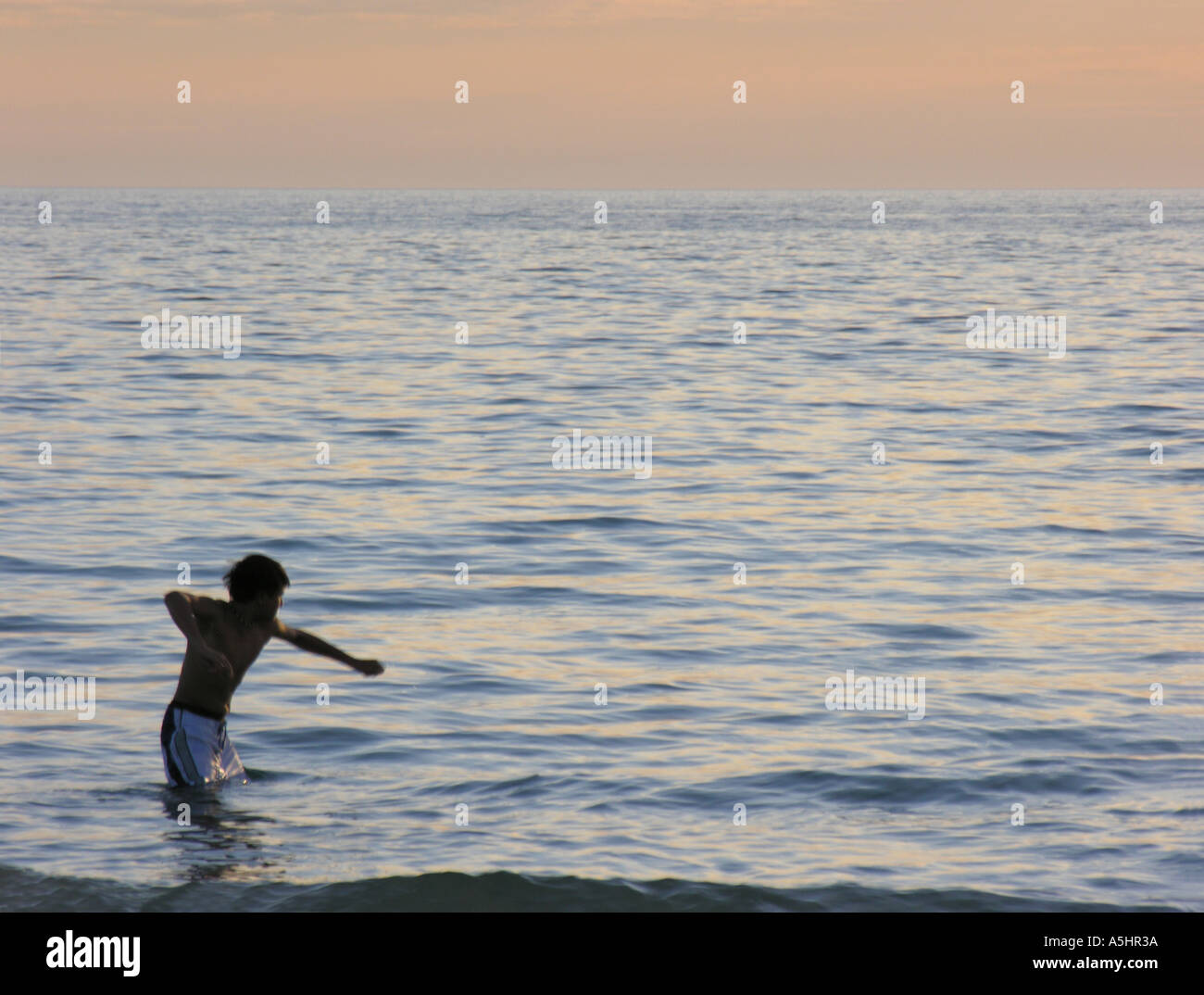 Boy standing in sea throwing pebble at dusk Stock Photo - Alamy