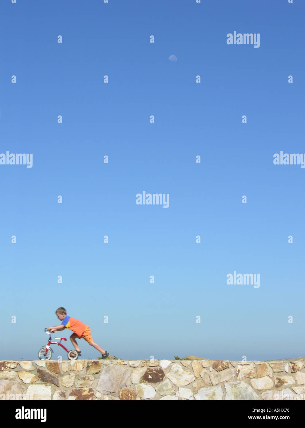 Young boy pushing tricycle on stone wall Stock Photo - Alamy