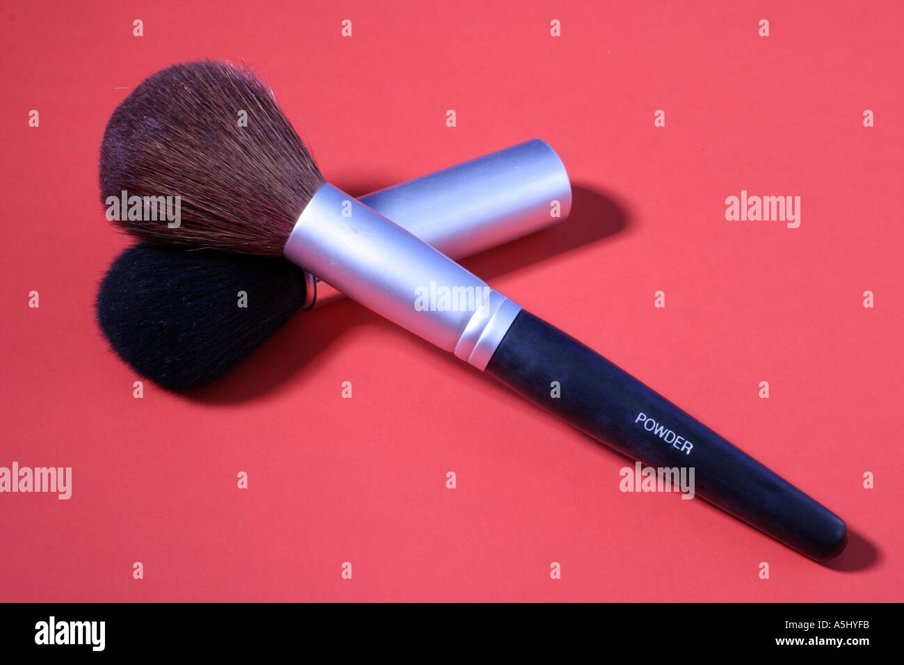 two powder brushes crossed on a red background Stock Photo - Alamy