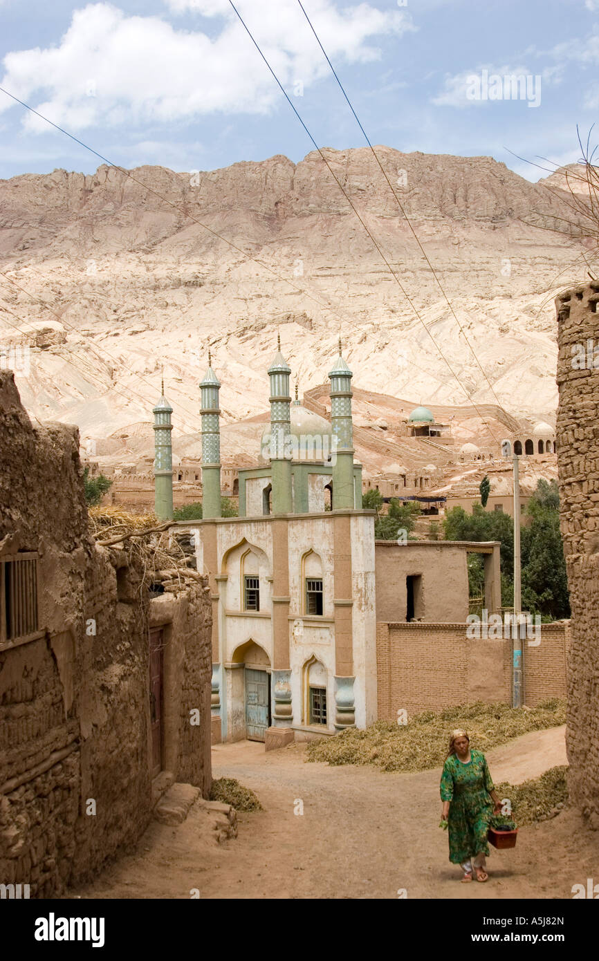 Uigur woman walks up the hill from the Mosque at Tuyok near Turpan ...