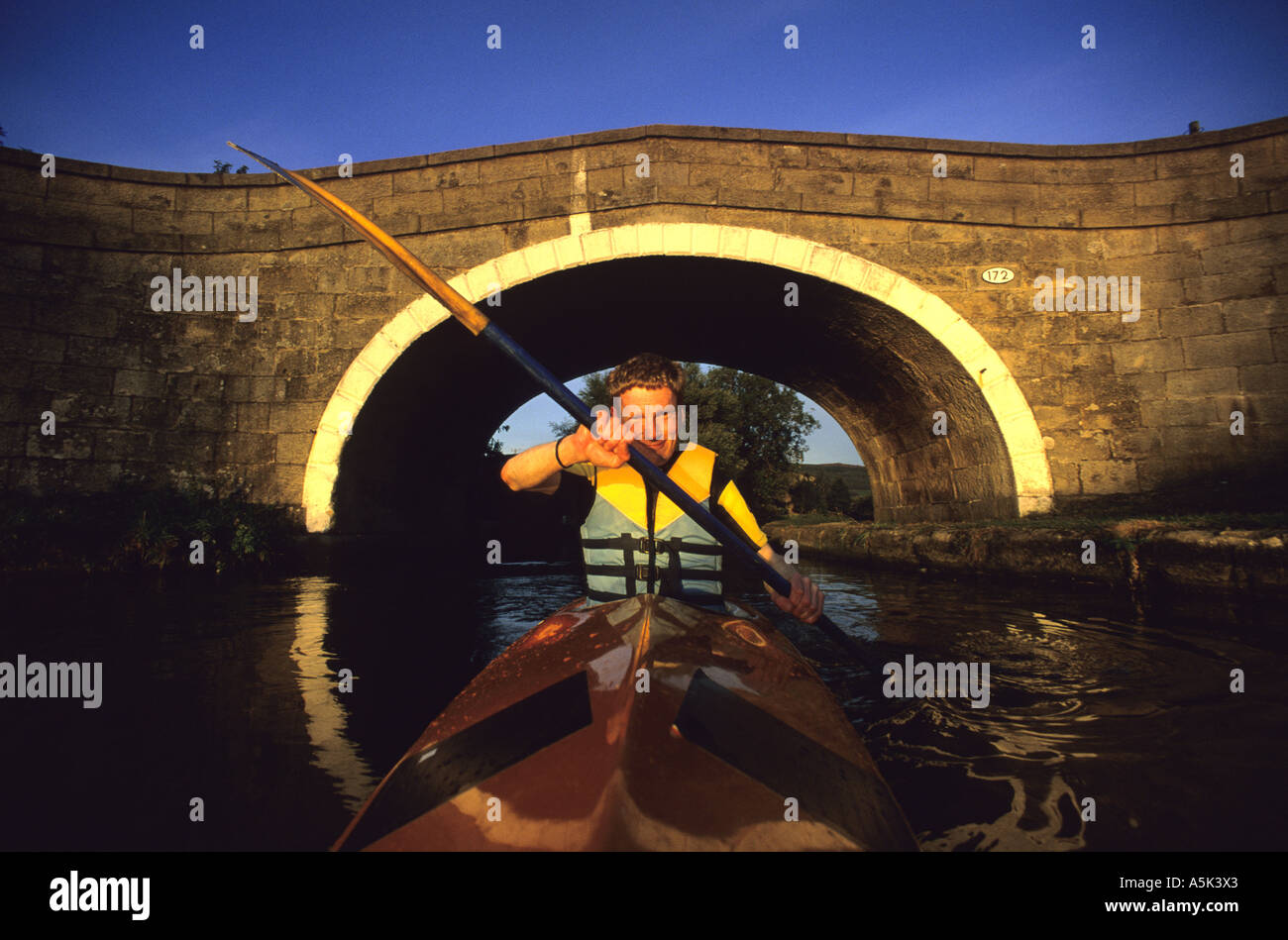 man paddling canoe through bridge on the leeds liverpool canal flowing ...