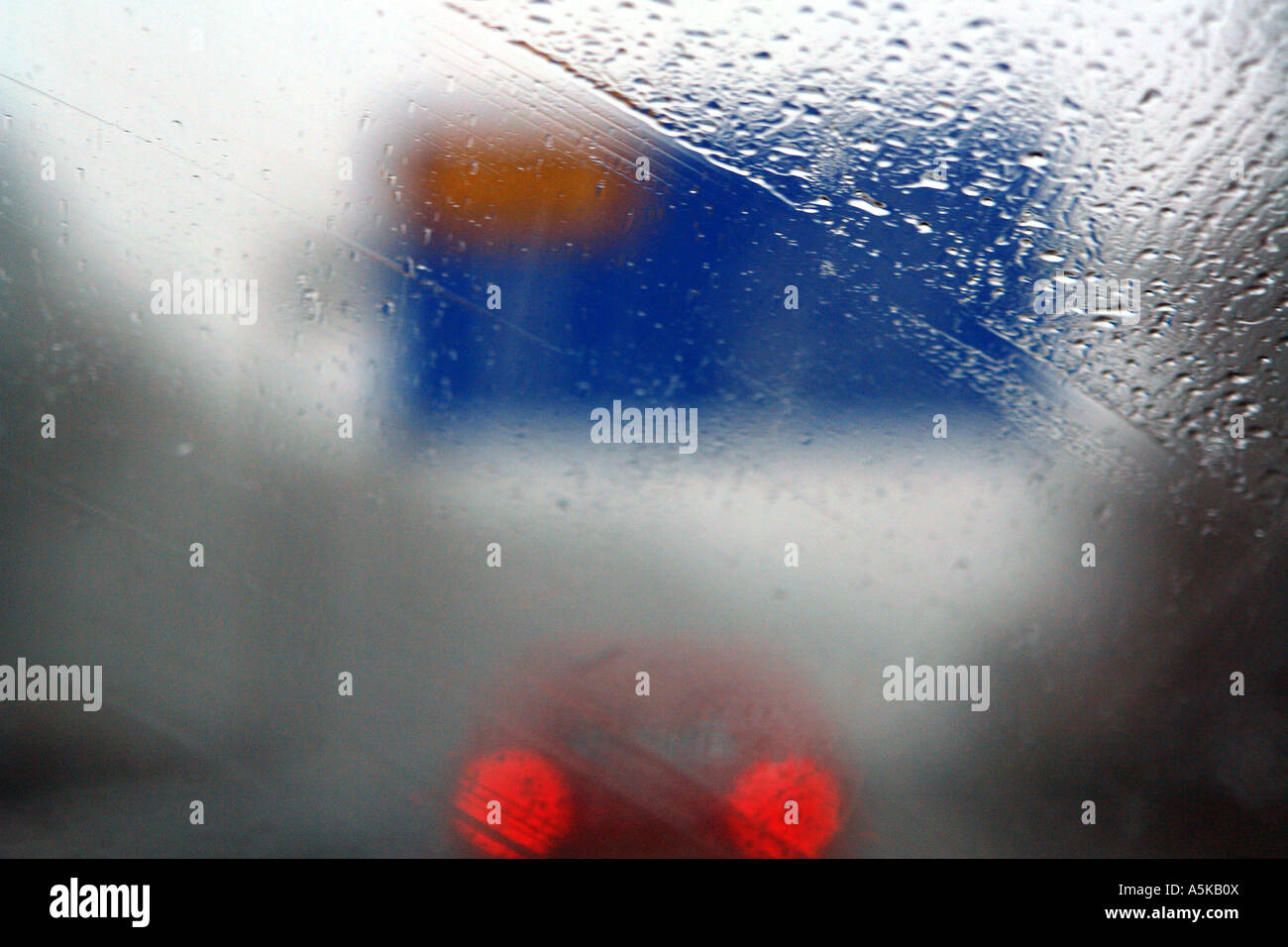 Look through wet windscreen on blurred blue sign board and back lights ...