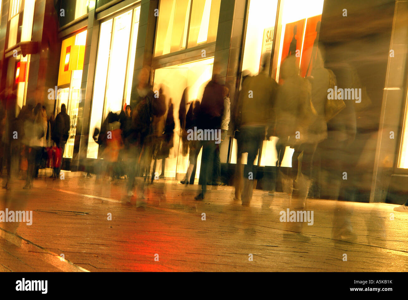 Night shot of blurred passers-by in front of brightly lit shop windows ...