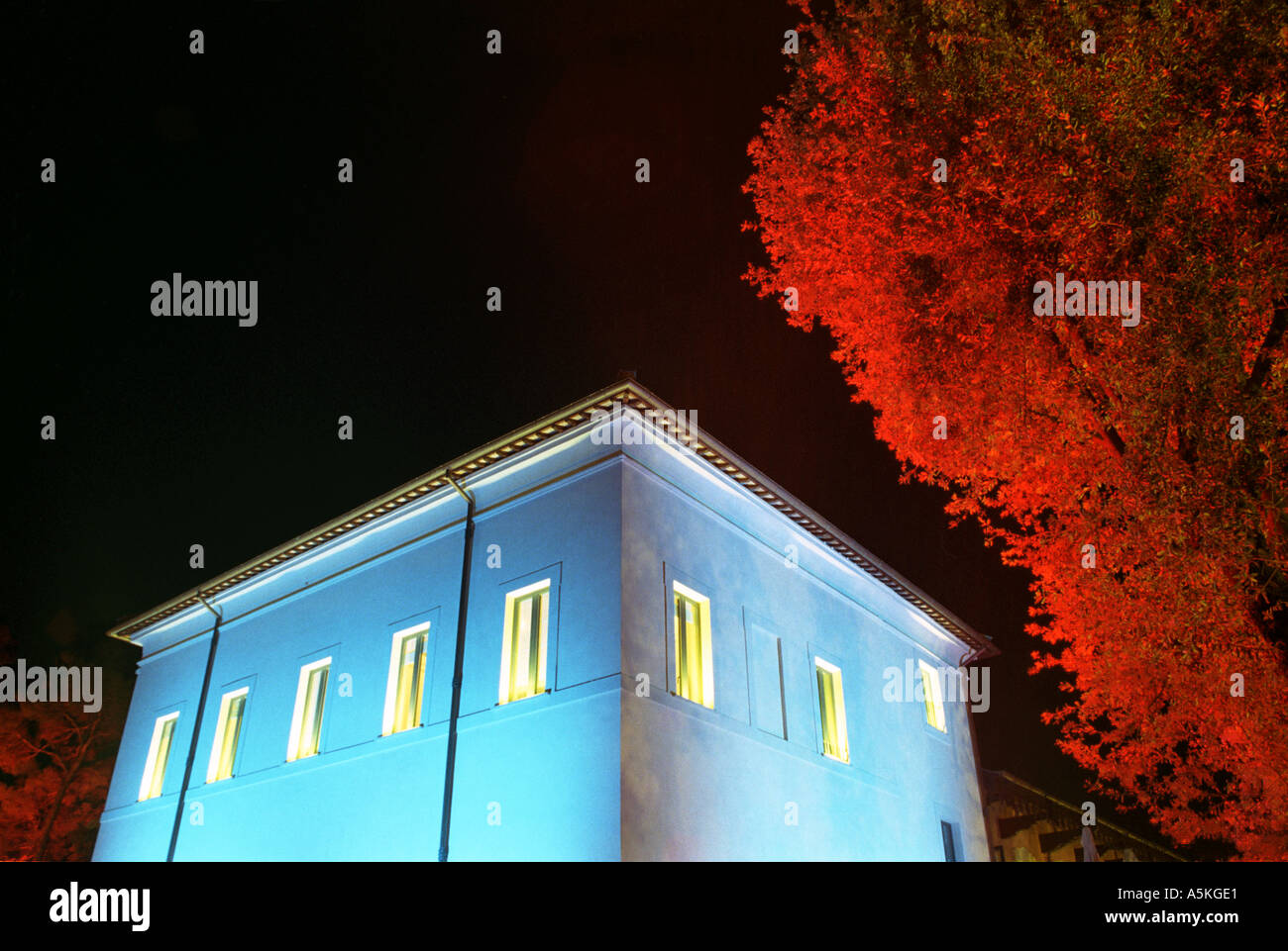building lit with blue spotlights at night with red trees Stock Photo ...