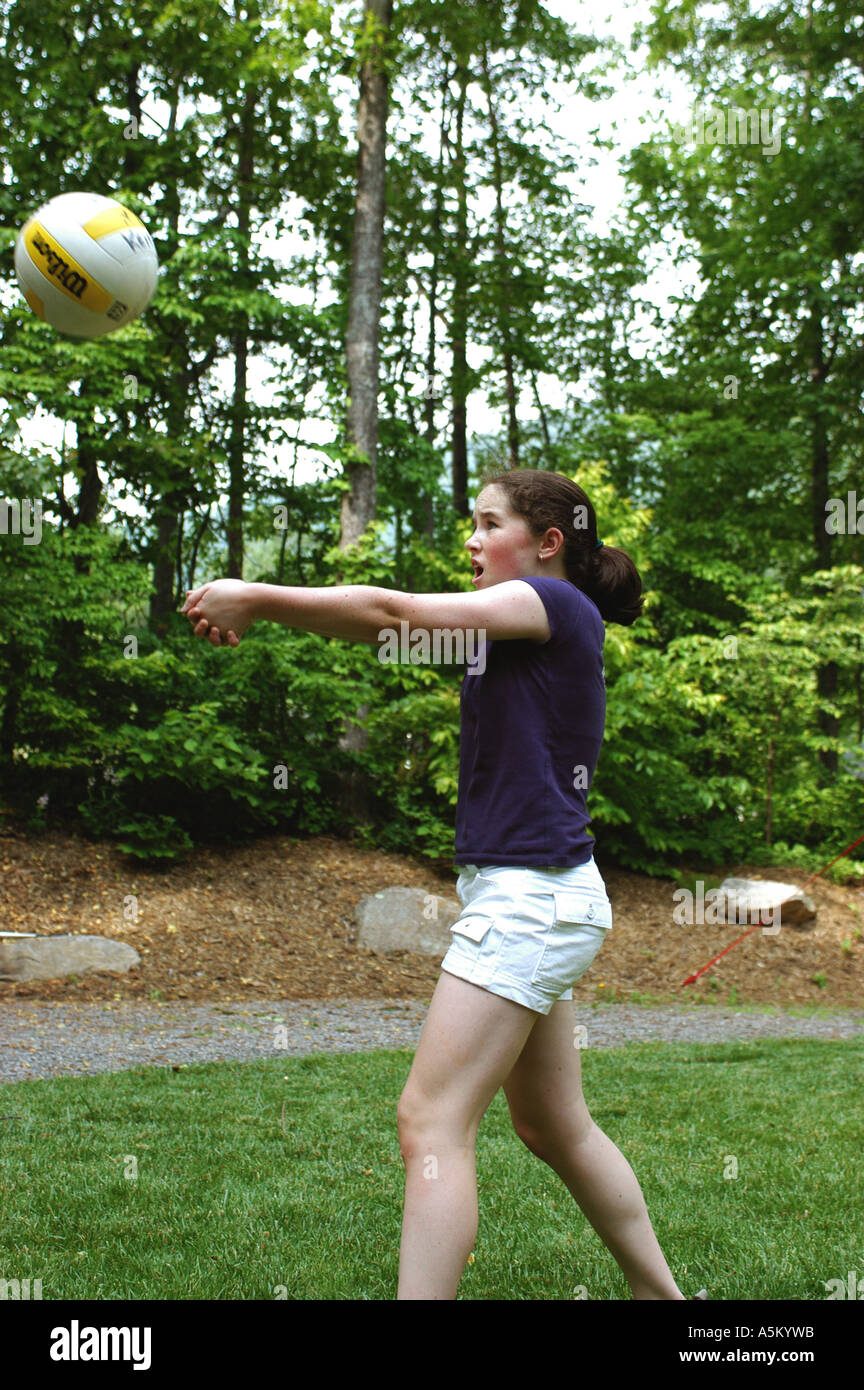 A pre teen girl is practicing volleyball in her yard as she sets the ...