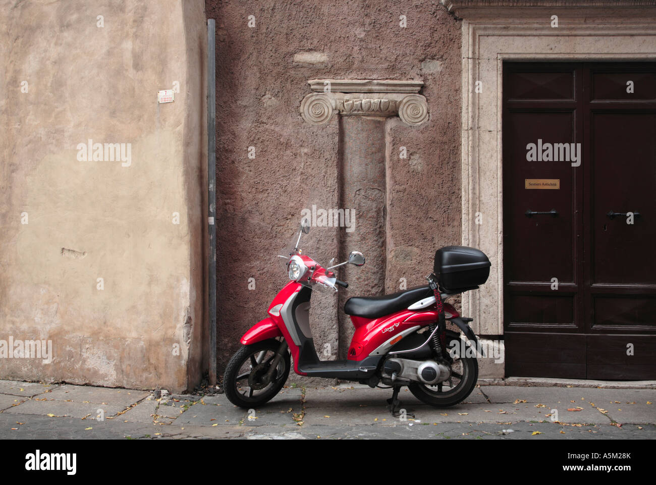 Red Moped parked in front of a piece of Roman Architecture embedded ...