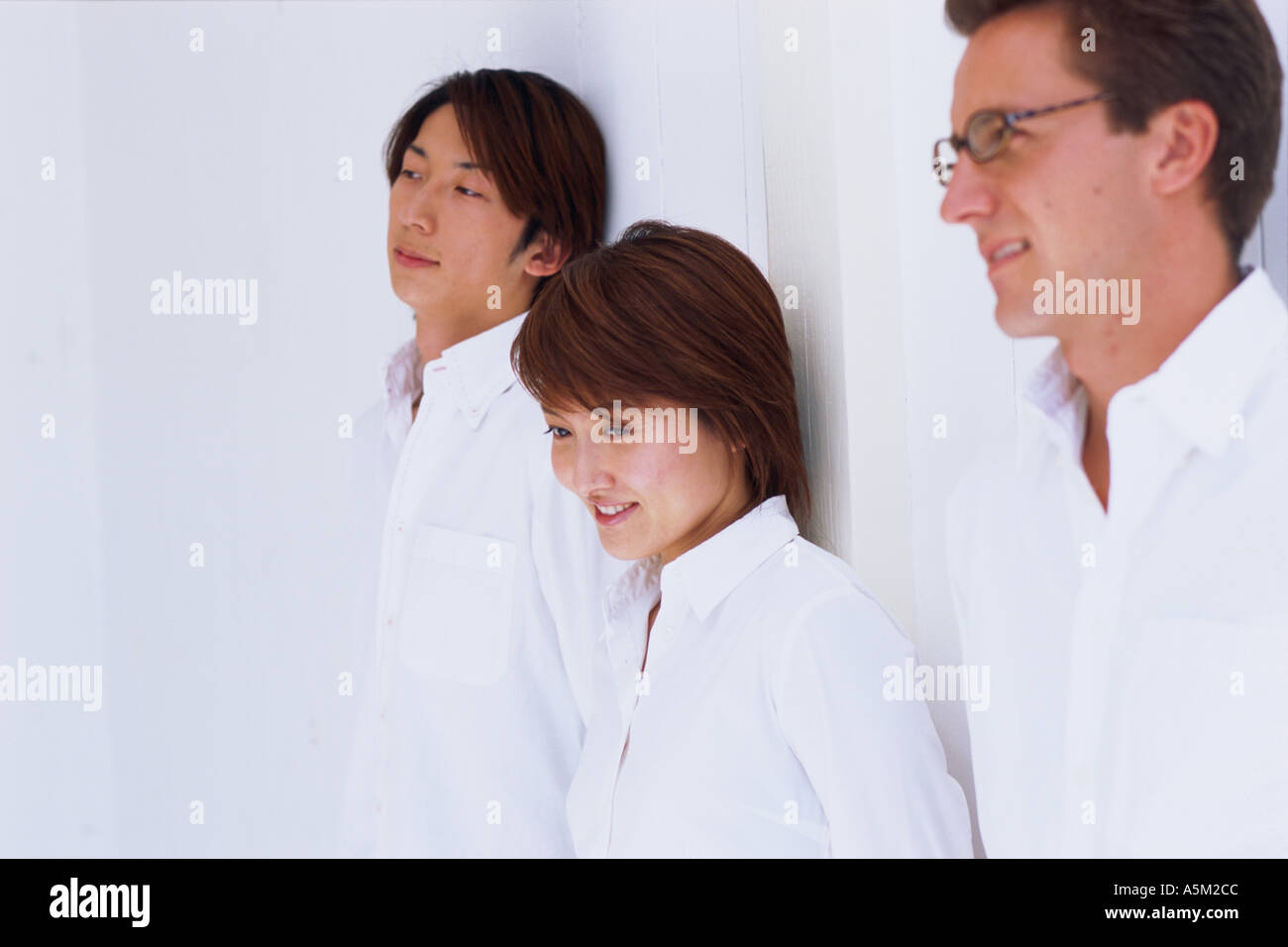 A woman and two men leaning against a wall Stock Photo - Alamy
