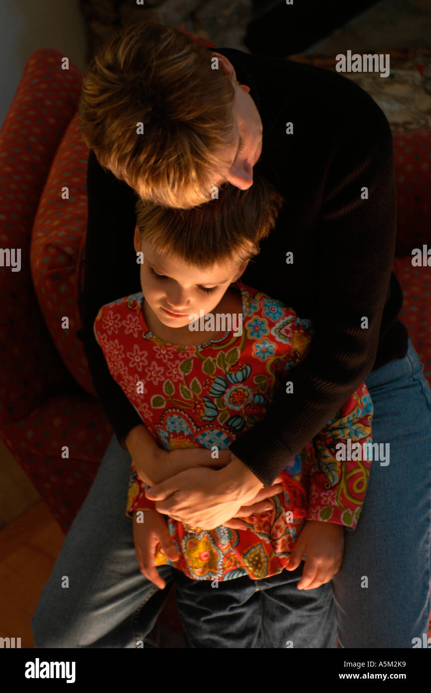 A six year old girl leans back against her mother who is sitting on the ...