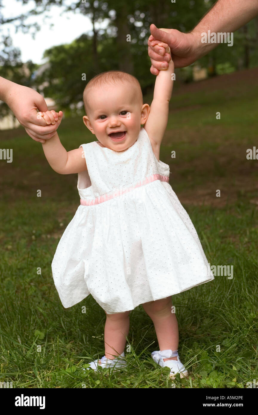 A six month old baby girl is standing up with the help of some older ...