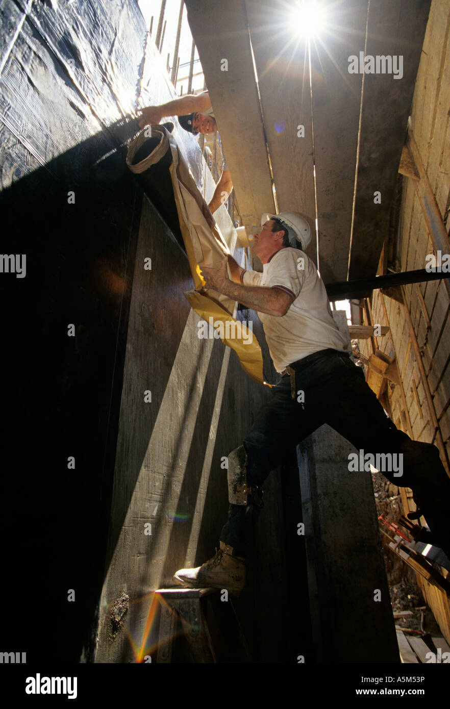 Workers install W R Grace Bituthene waterproof membrane on foundation ...