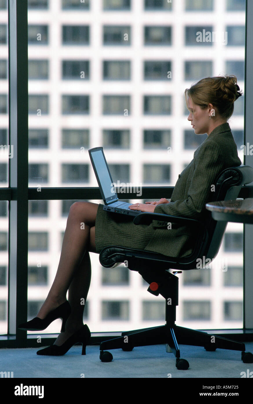 female executive works on portable computer in hi rise office building ...