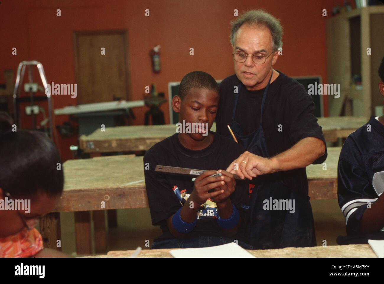 Teacher works with students in wood shop class at an inner city high ...