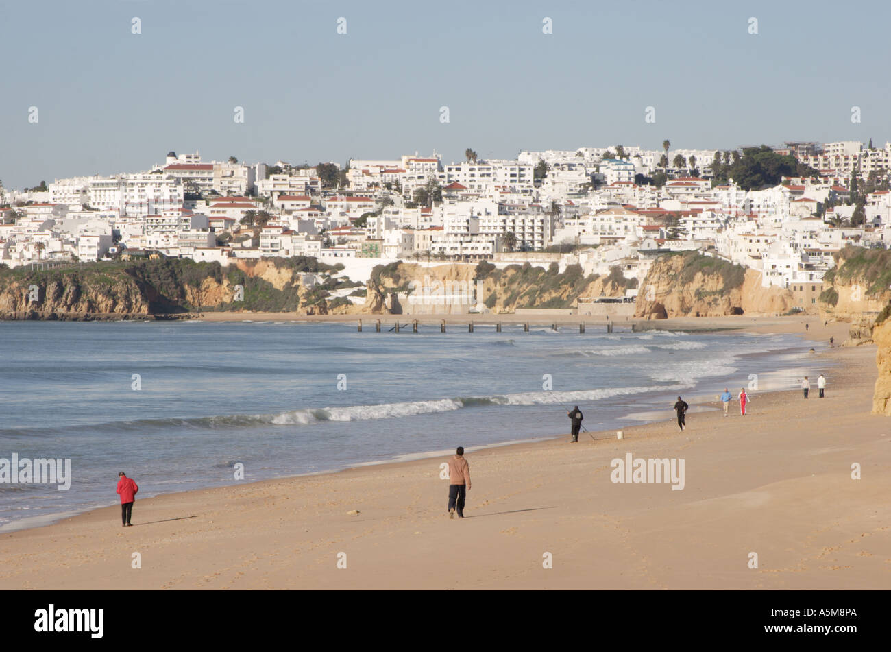 People walking along a sandy beach with the town of Albufeira in the ...