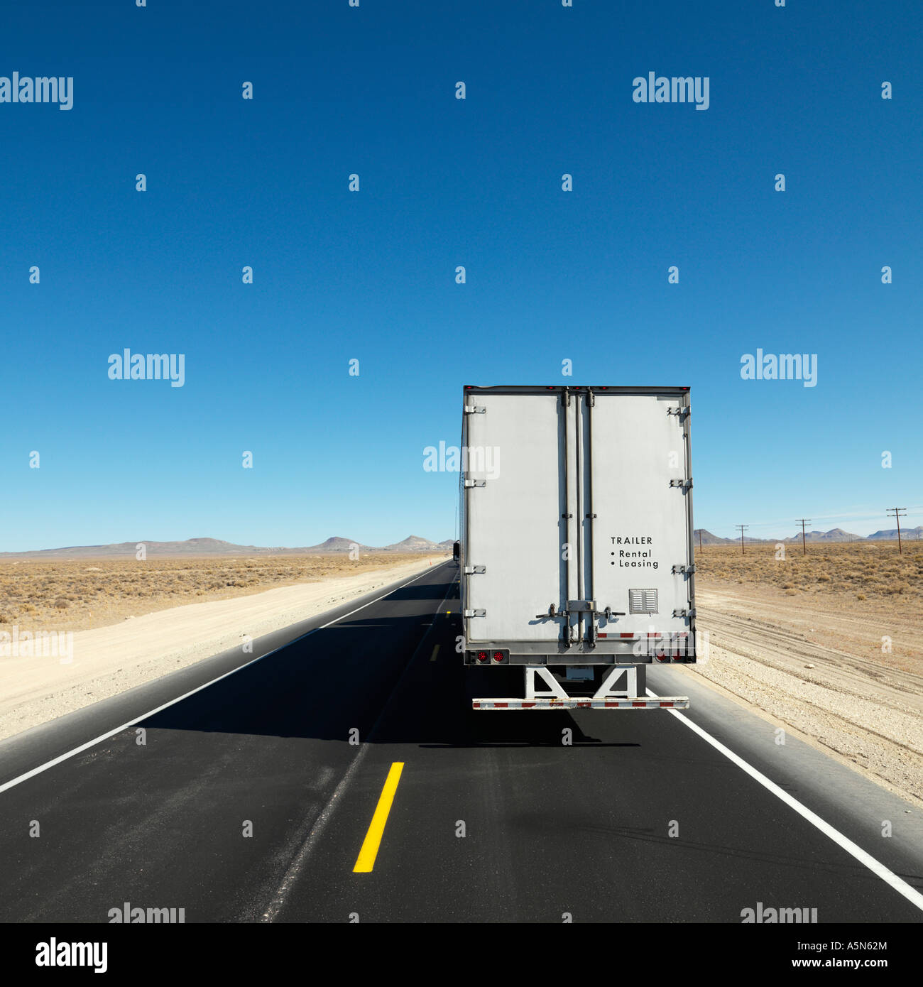 Back view of semi truck traveling down highway towards horizon under ...
