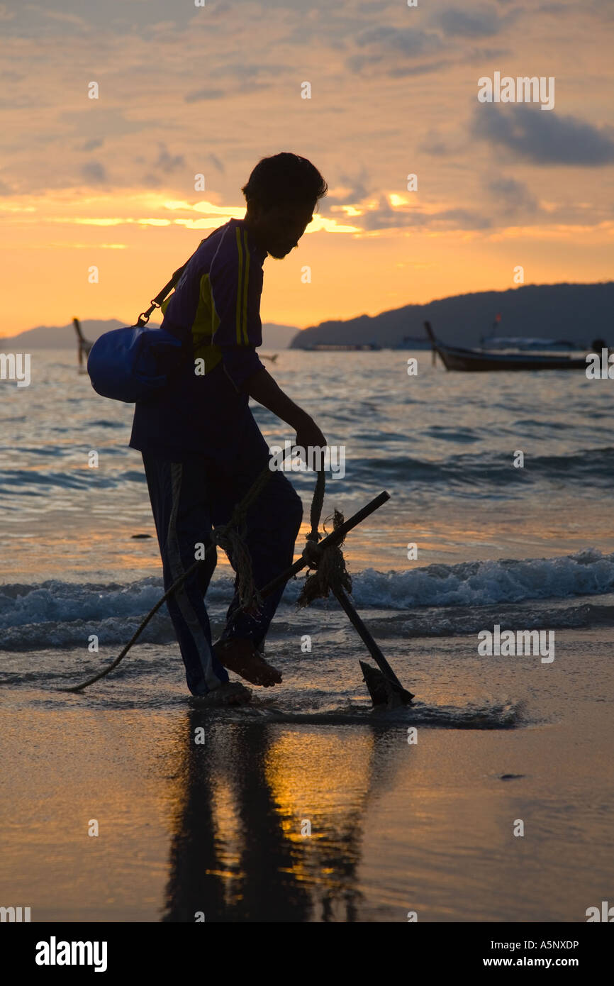 Boatman lifting anchor of long tail boat at sunset Krabi province beach ...