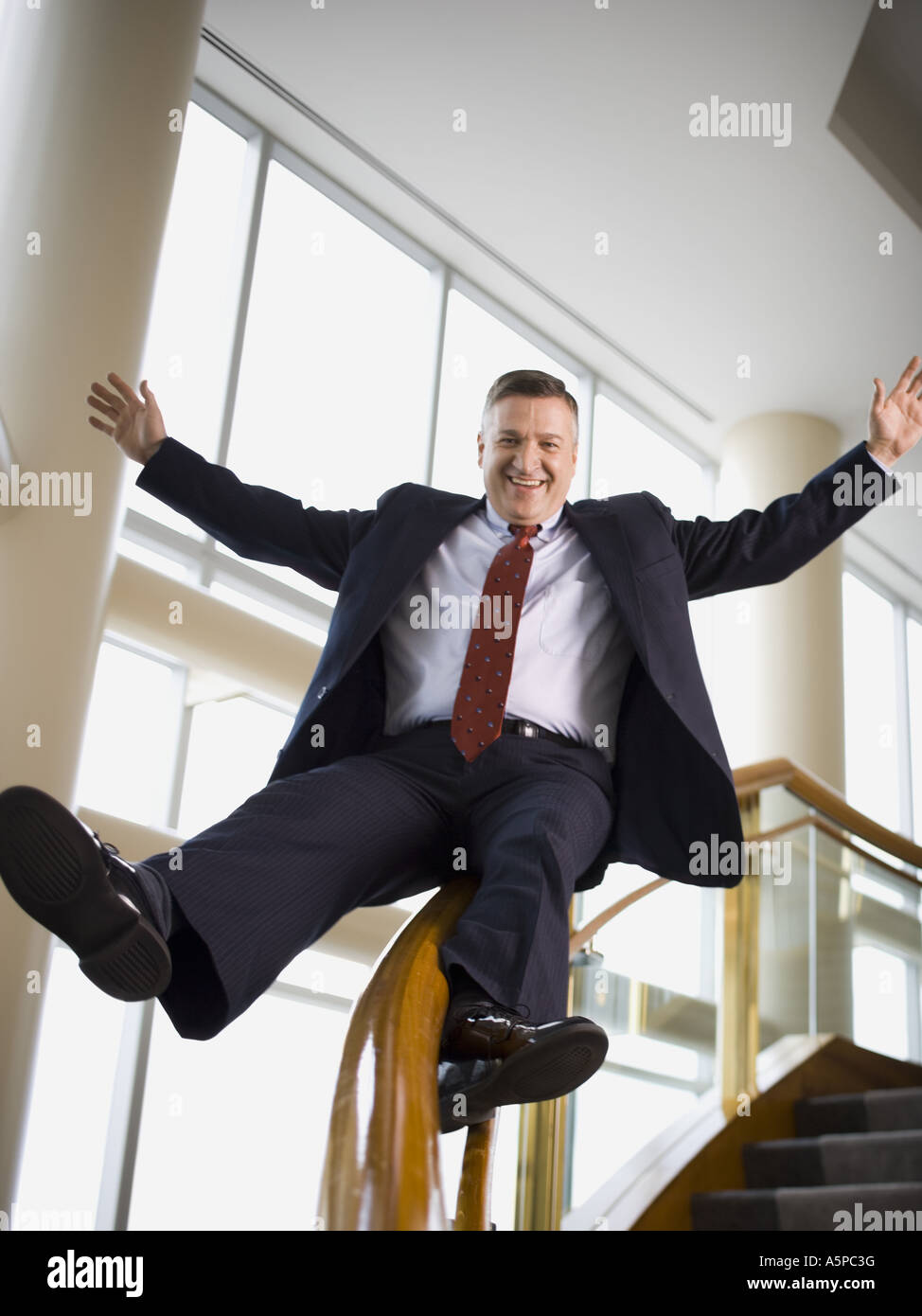 Happy businessman sliding down stair railing Stock Photo - Alamy