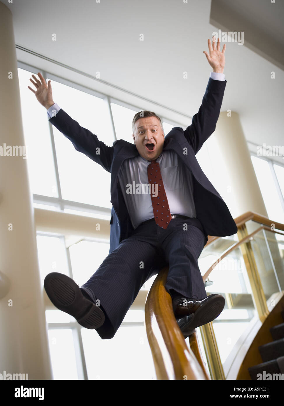 Happy businessman sliding down stair railing Stock Photo - Alamy