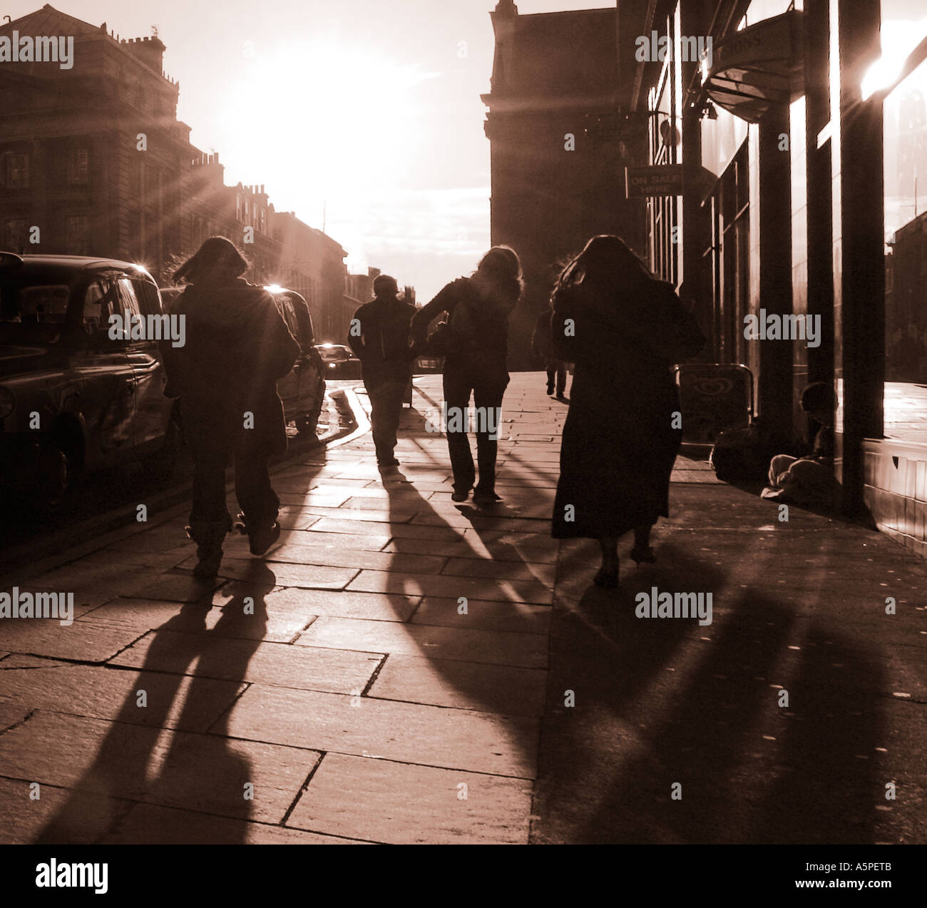 Pedestrians walking uphill in a city street towards the sun Edinburgh ...