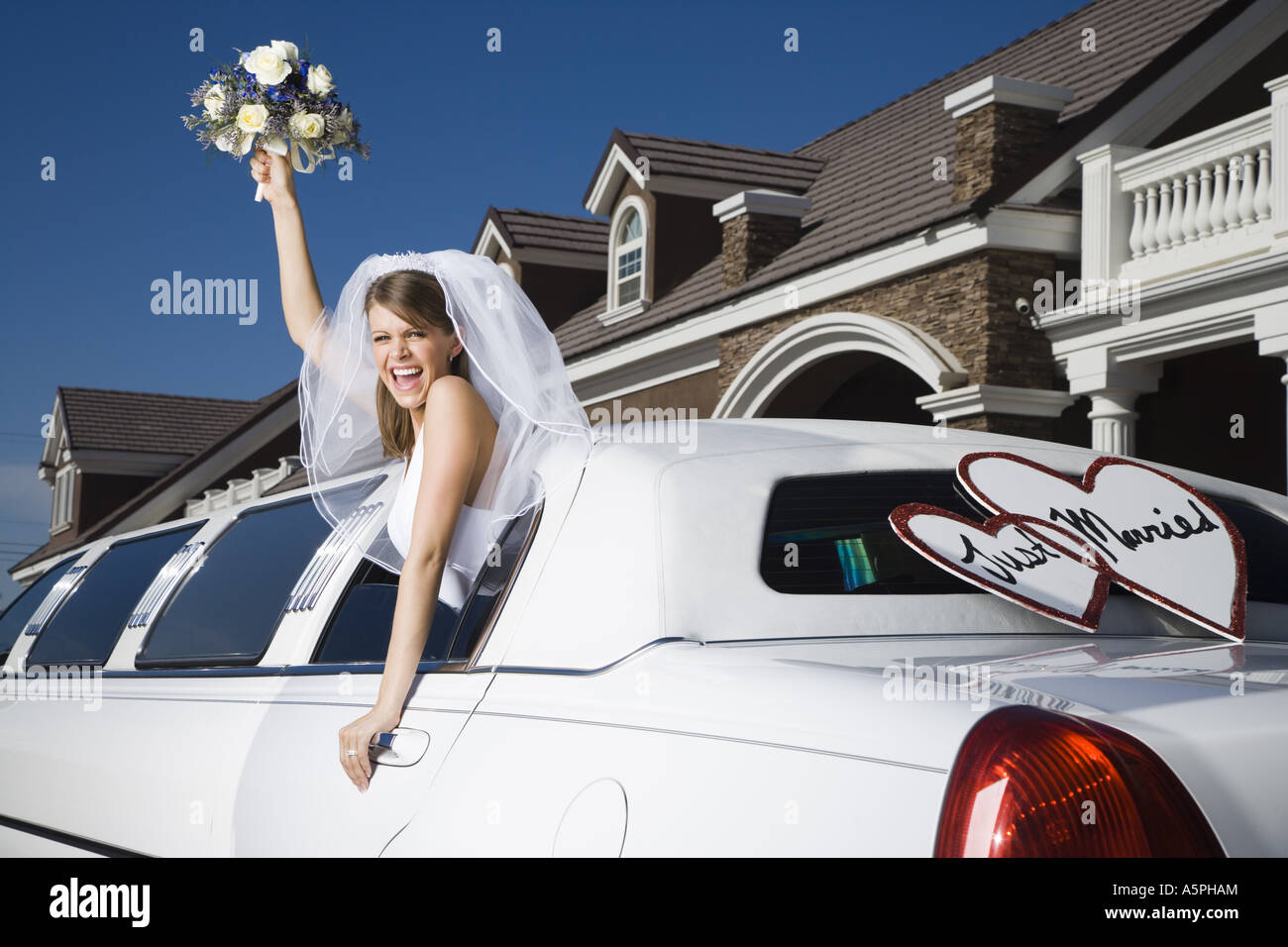 A bride holding a bouquet of flowers and leaning out of a limo window ...