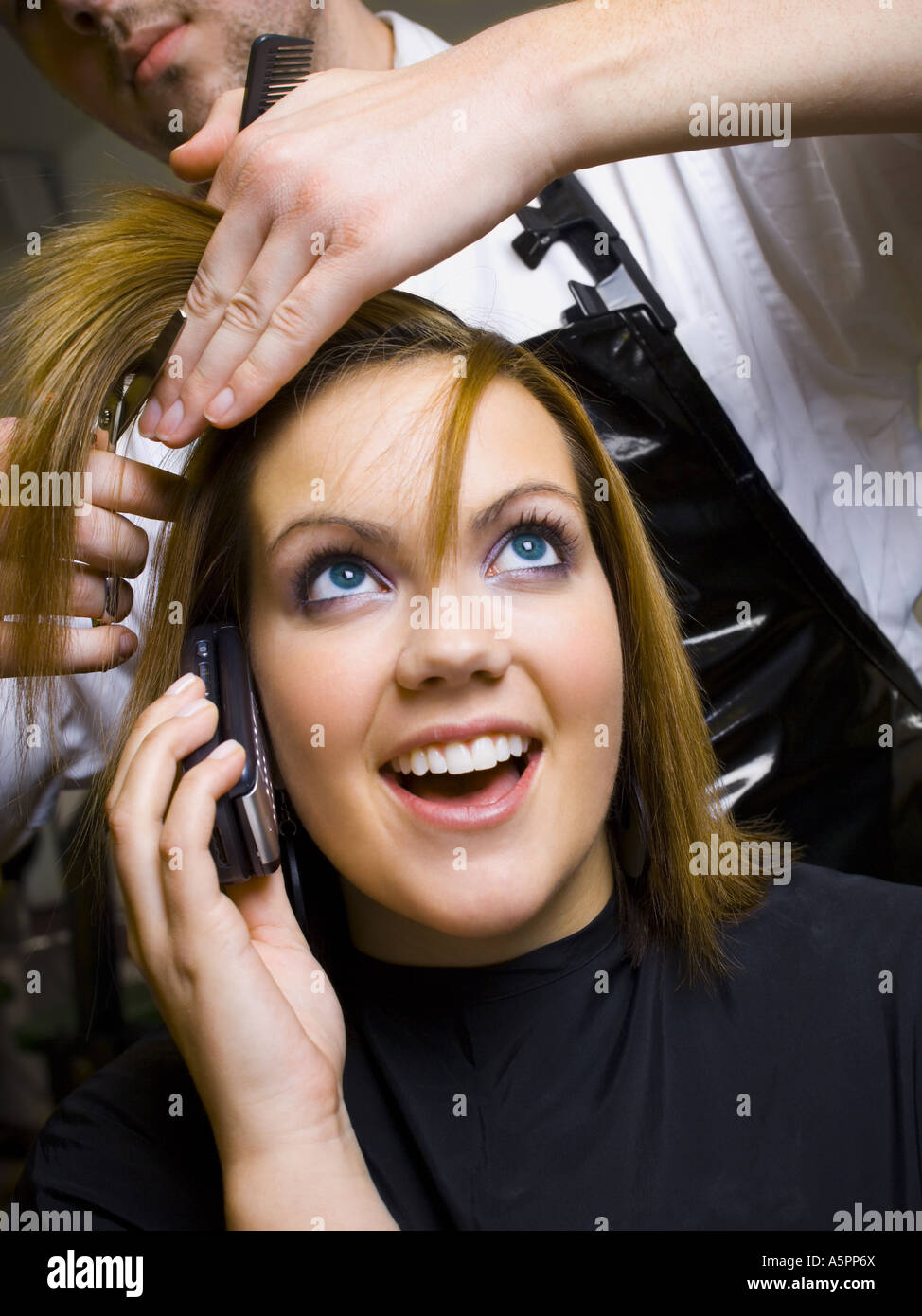 Woman on cell phone smiling while having hair cut Stock Photo - Alamy