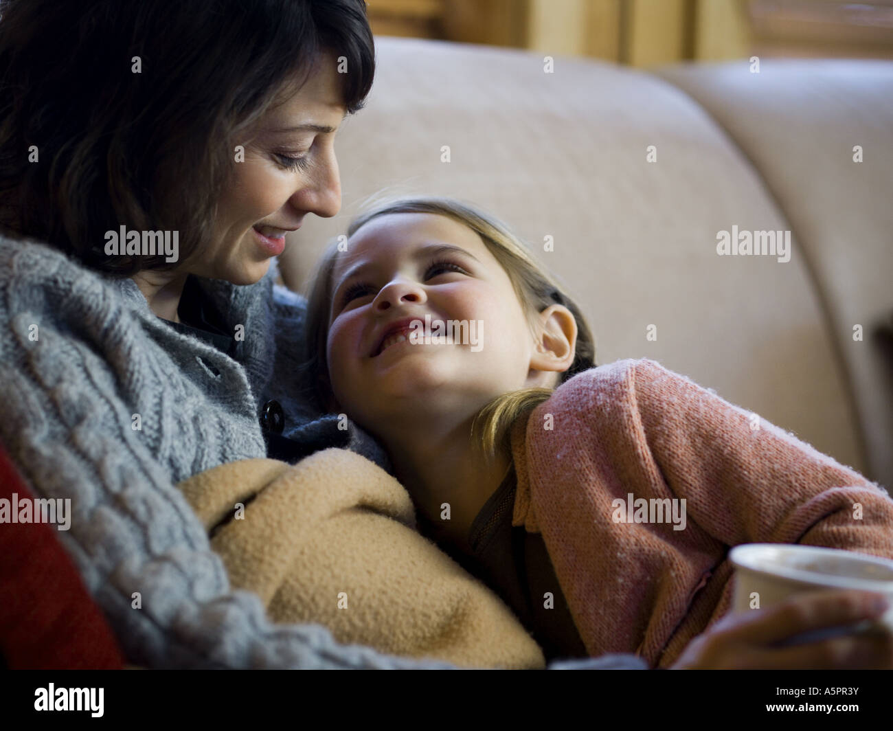 Woman with young girl snuggling on sofa Stock Photo - Alamy
