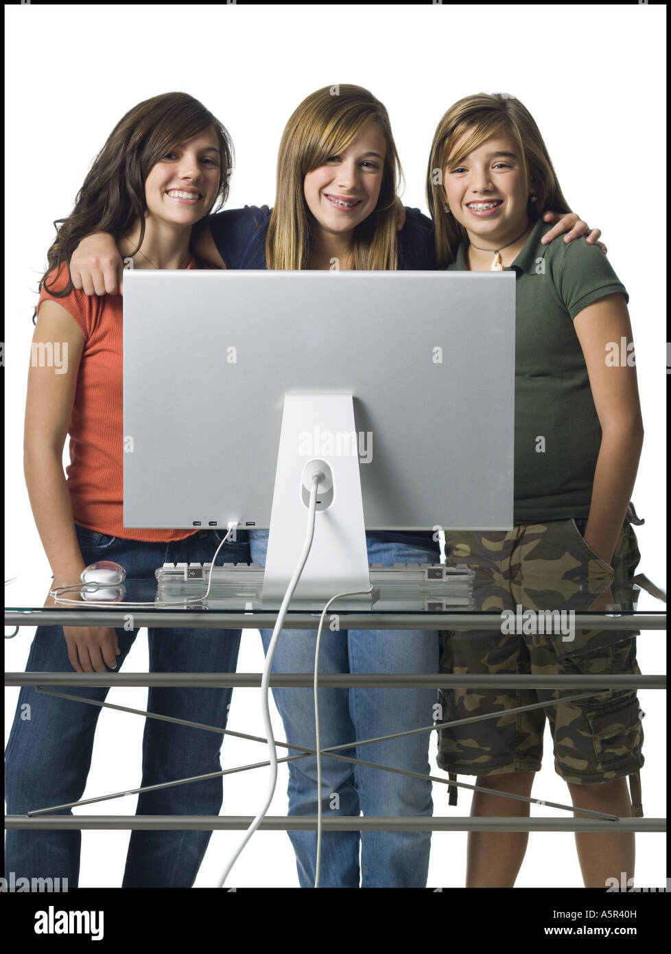 Three girls standing behind computer monitor smiling Stock Photo - Alamy