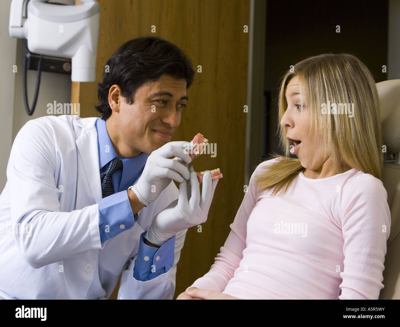 Male dentist holding false teeth talking to girl Stock Photo - Alamy