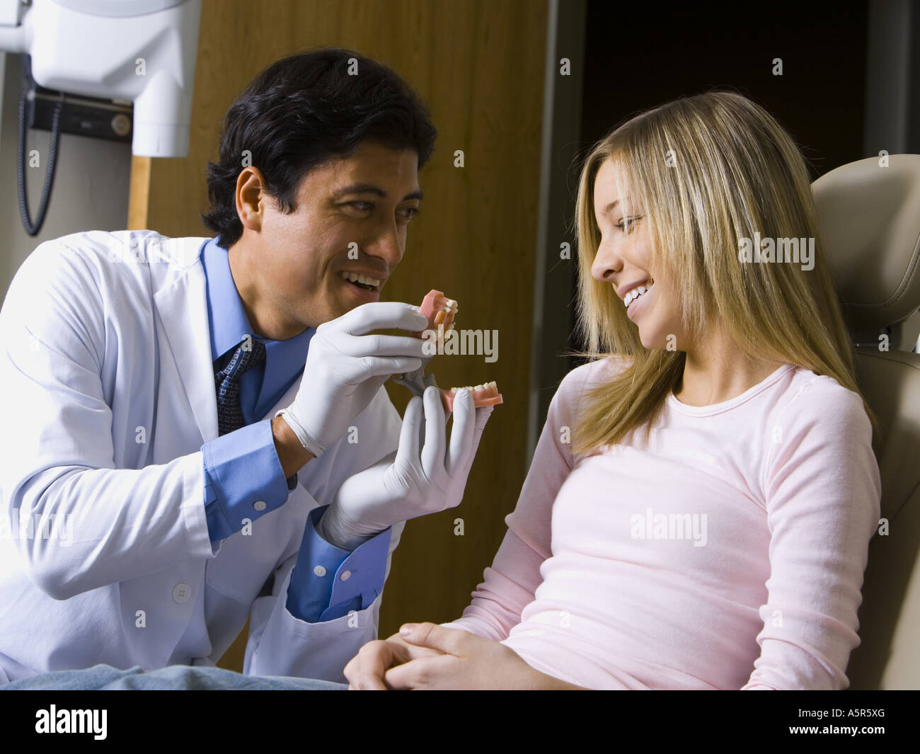 Male dentist holding false teeth talking to girl Stock Photo - Alamy