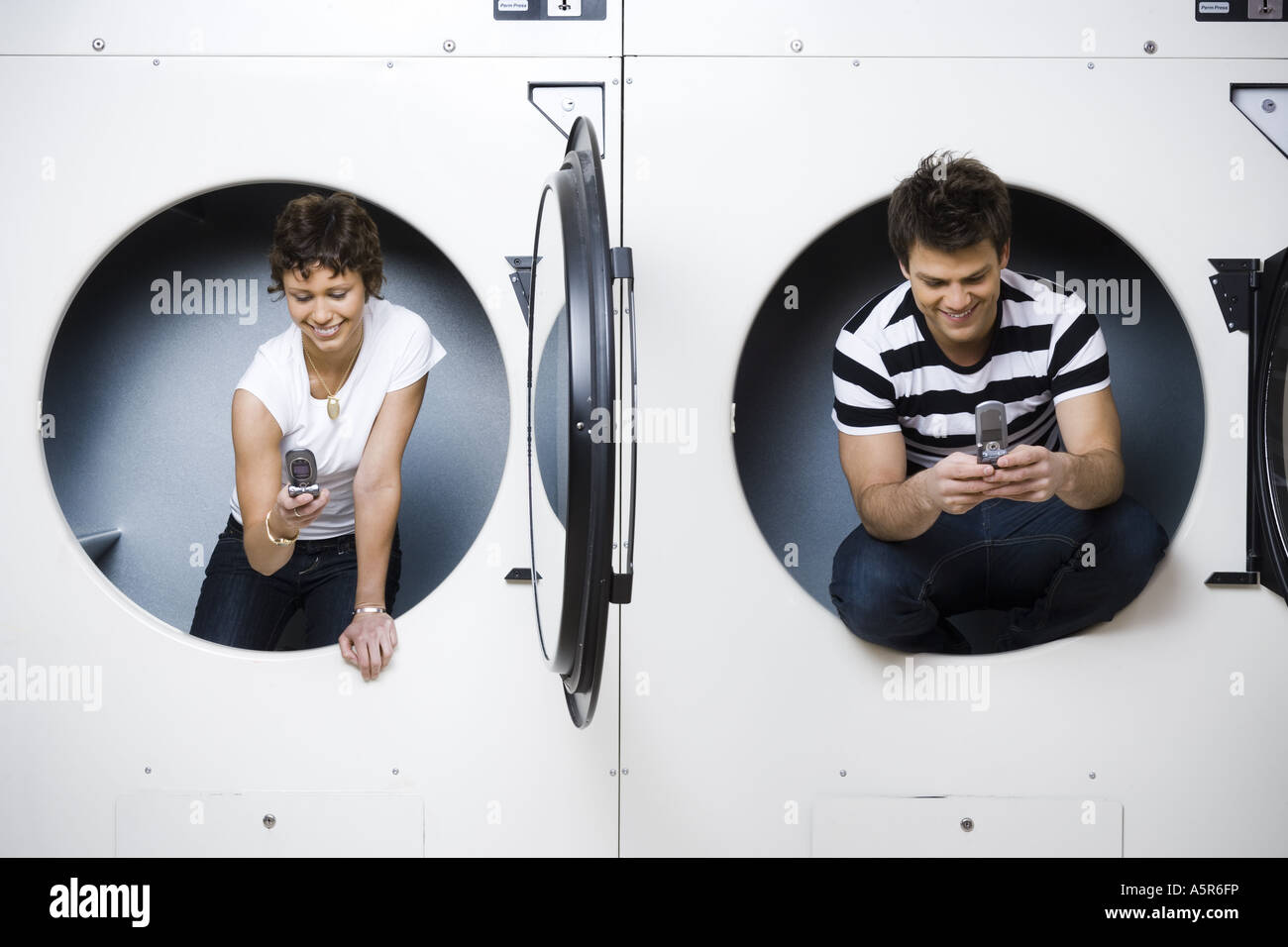 Two people in dryers at Laundromat with cell phones Stock Photo - Alamy