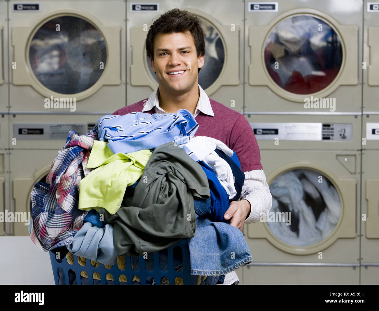 Man with clothing in laundry basket at Laundromat smiling Stock Photo ...
