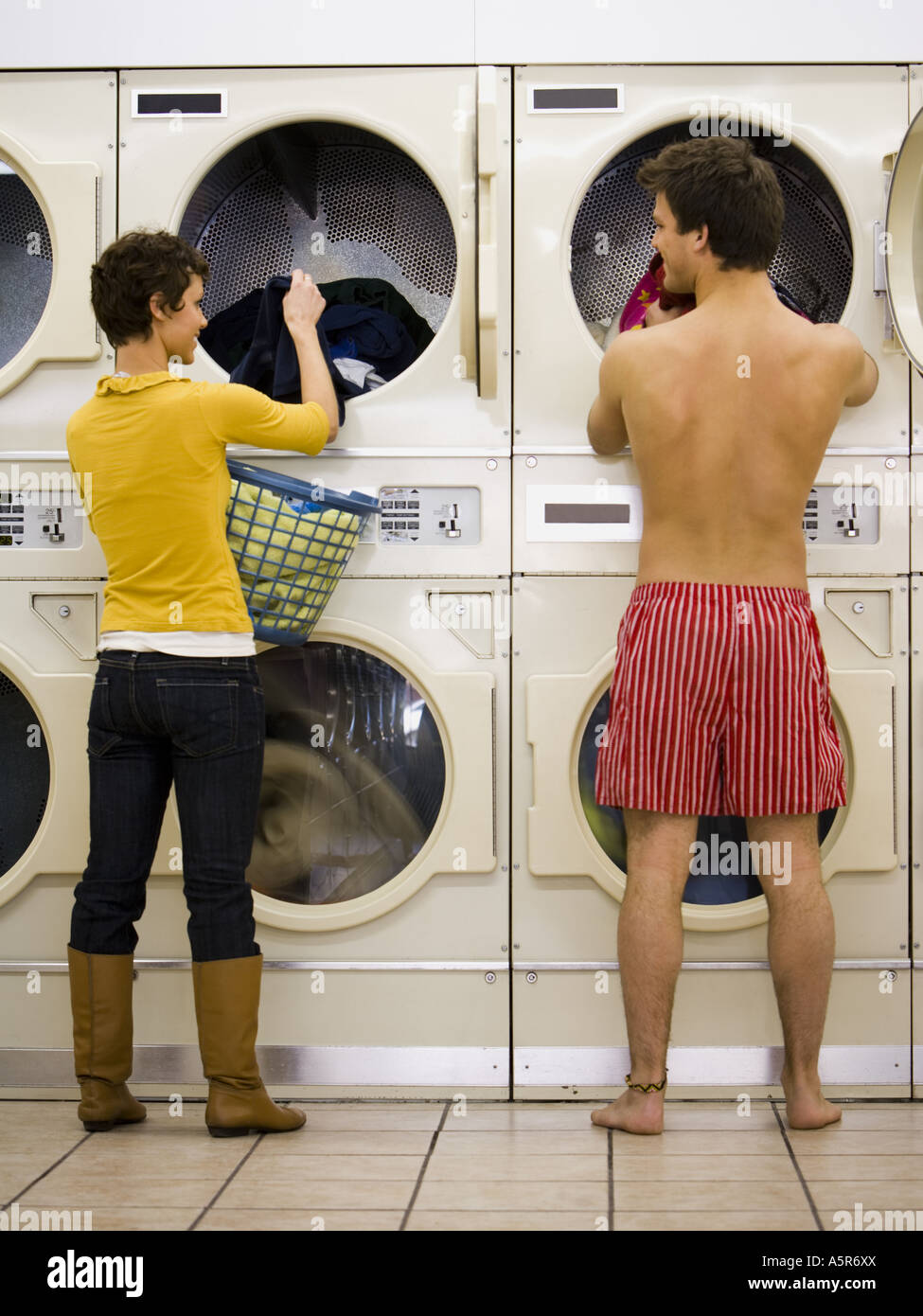 Woman and man in boxers removing clothing from dryers at Laundromat ...