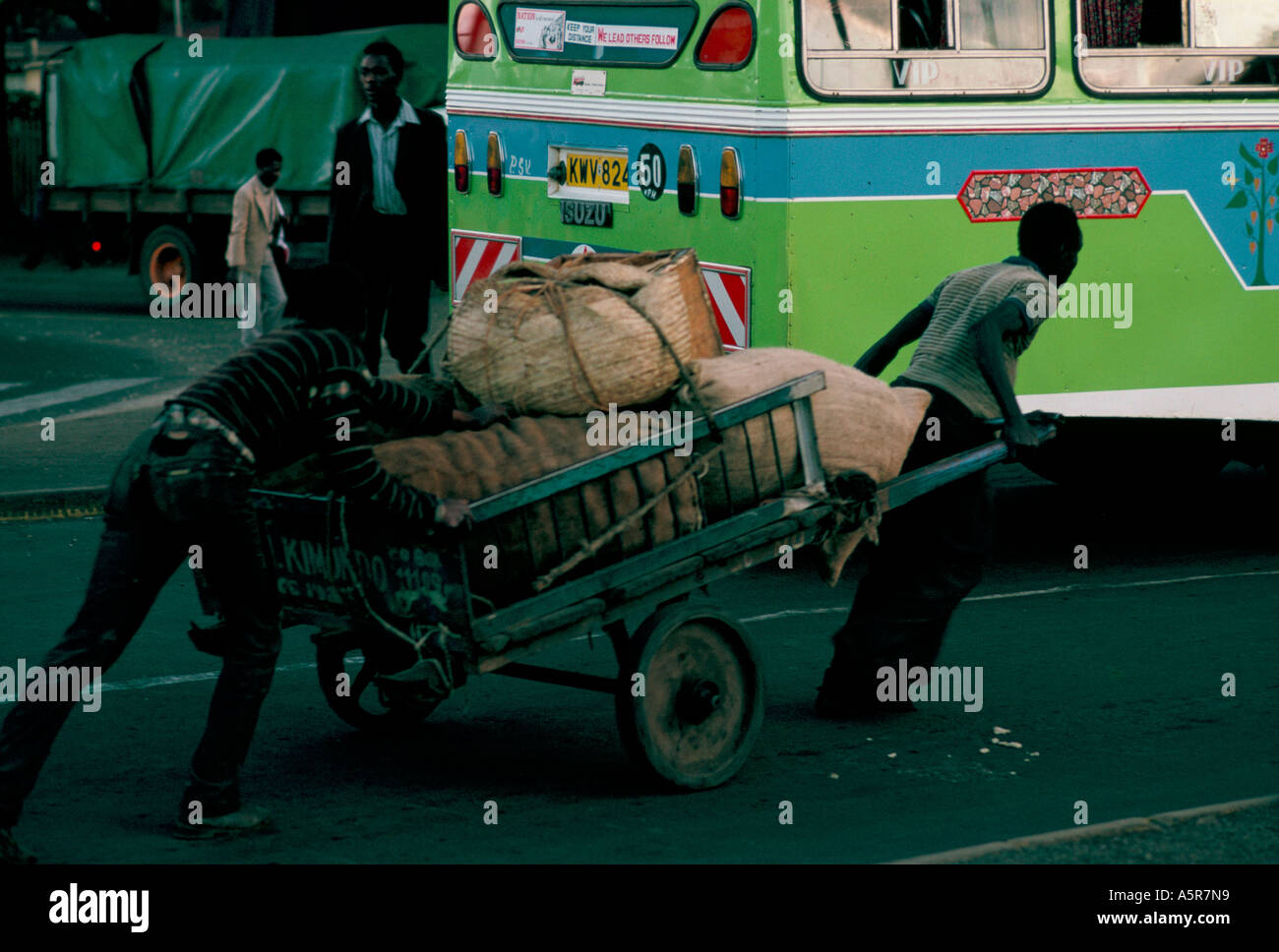 TWO MEN PULLING A CART LOADED WITH SACKS ON A BUSY STREET BESIDE A ...