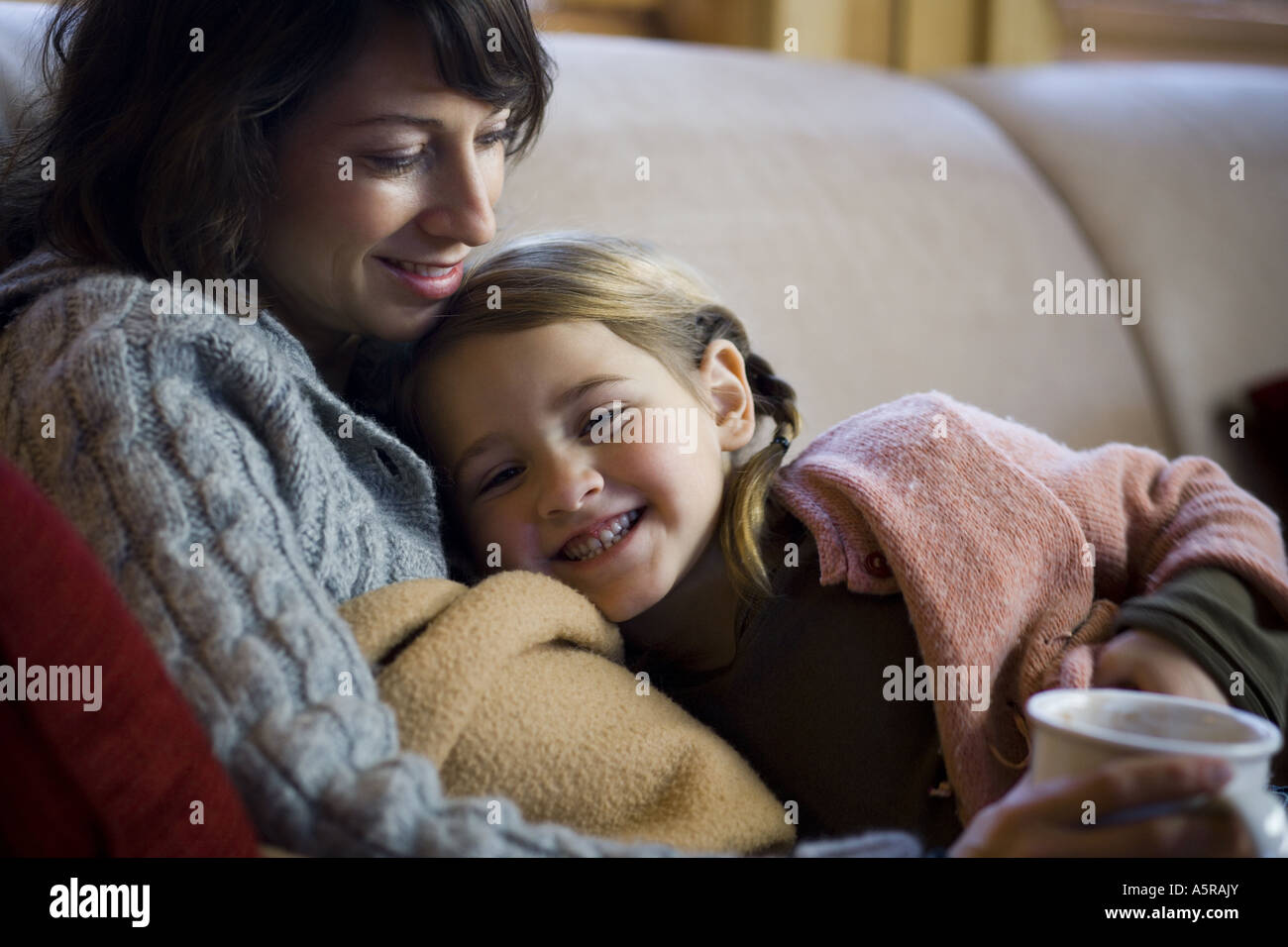 Woman with young girl snuggling on sofa Stock Photo - Alamy
