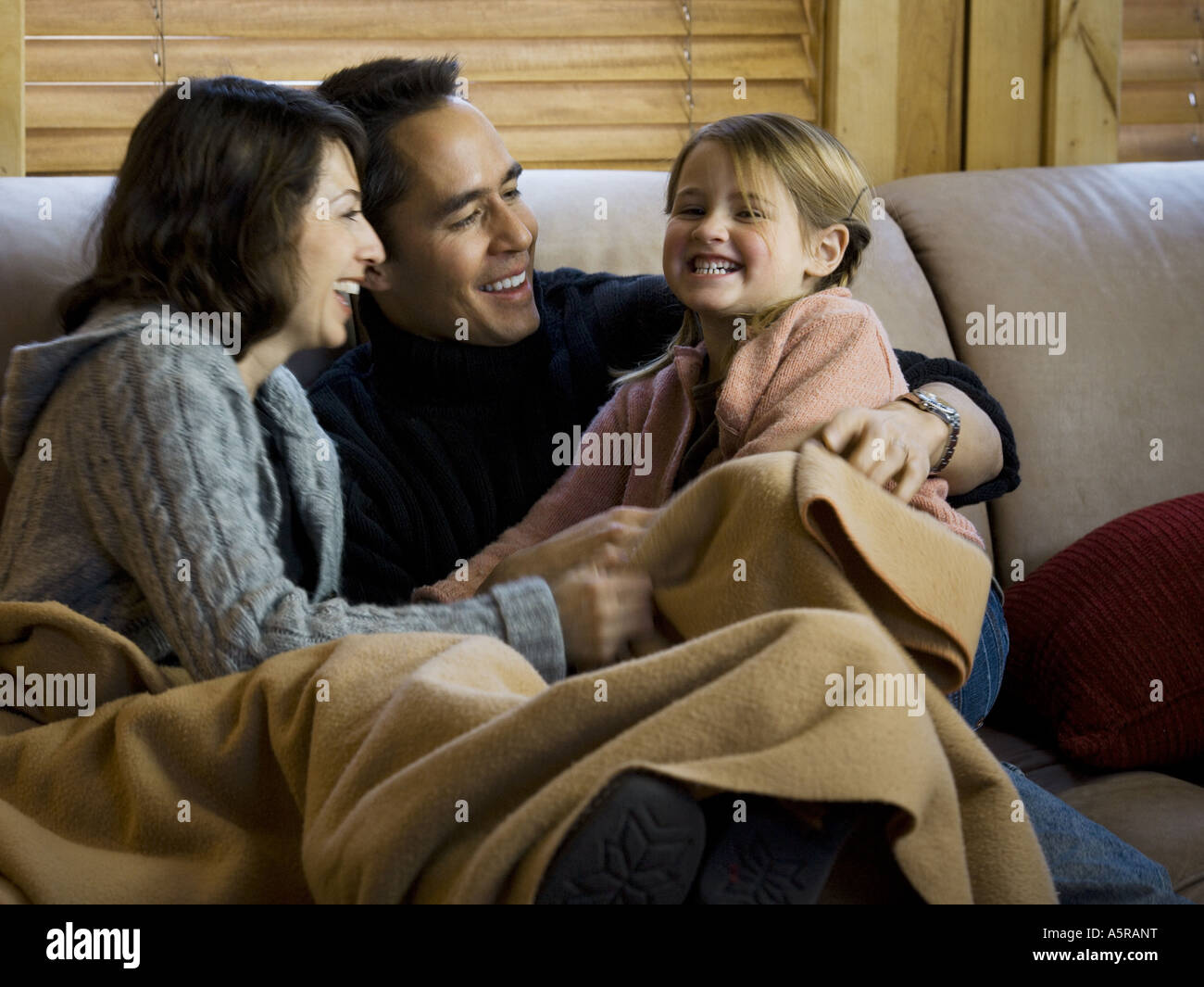 Man and woman snuggling with young girl on sofa with blanket Stock ...