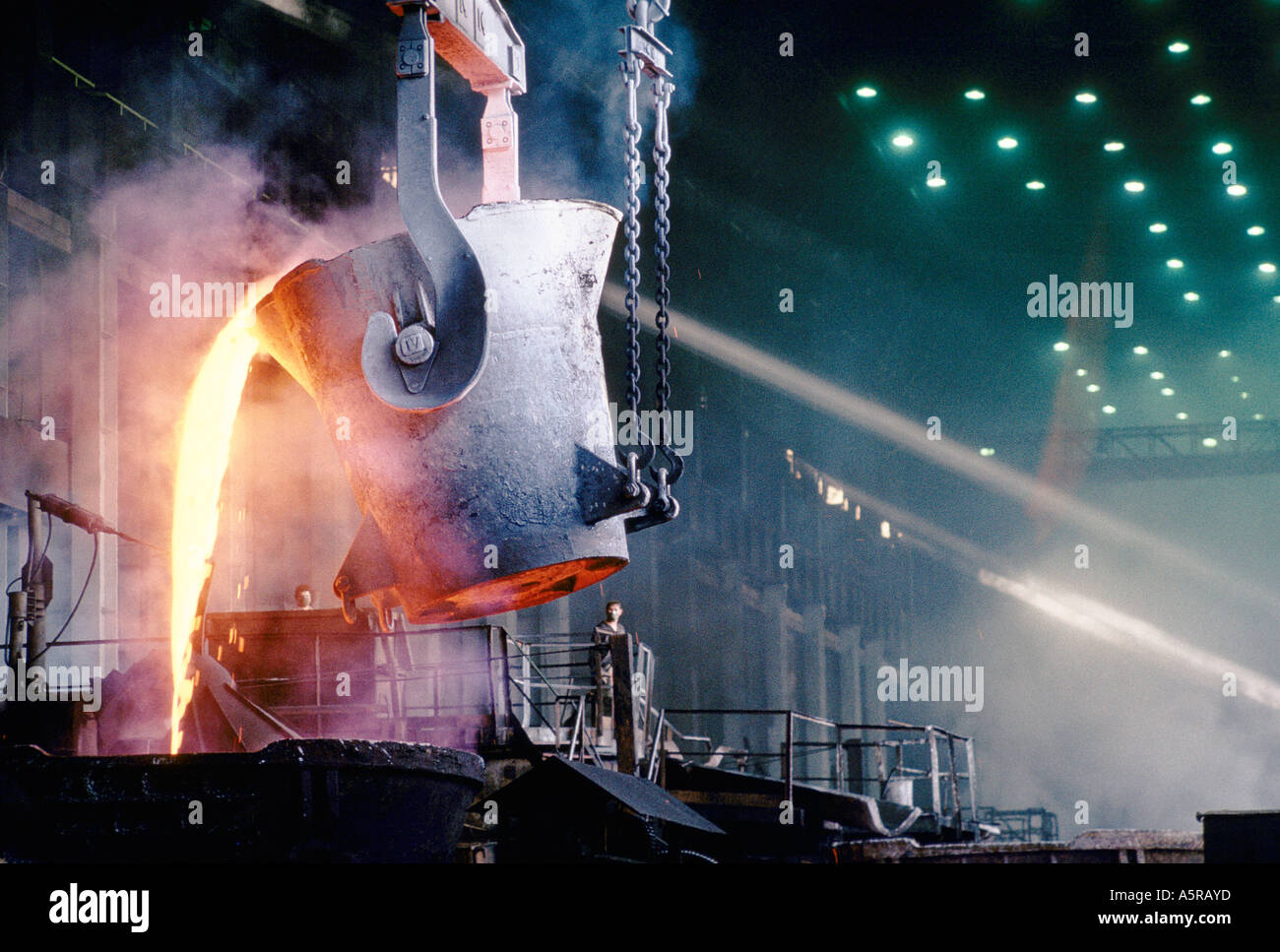Workers pouring molten copper from a large bucket hanging from ...