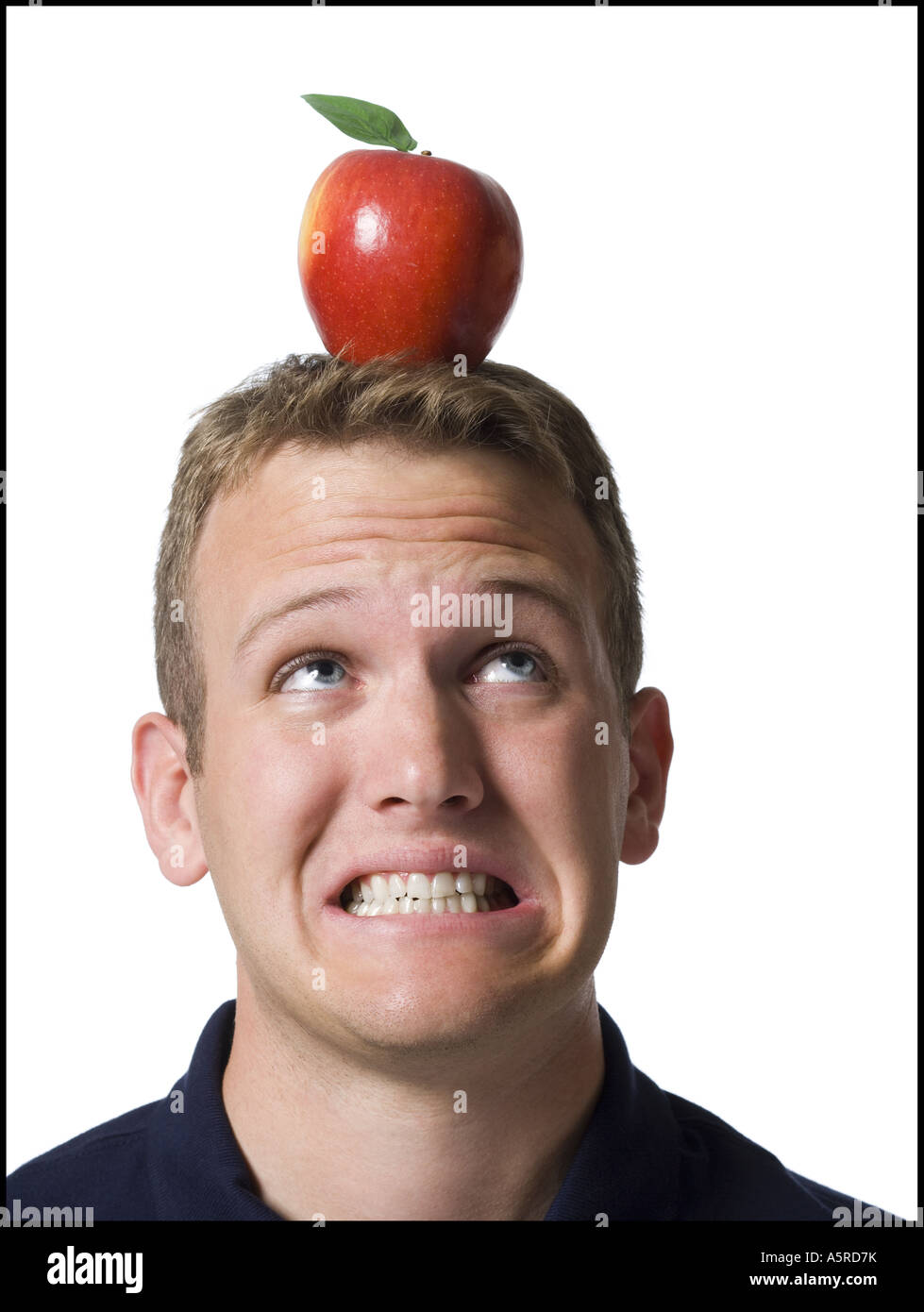 Close up of a young man clenching his teeth with an apple on his head ...
