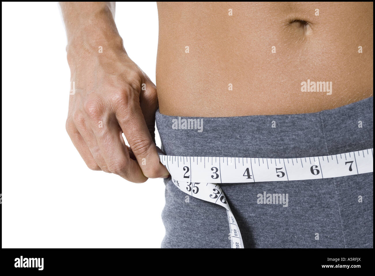 Mid section view of a young woman measuring her waist with a measuring ...